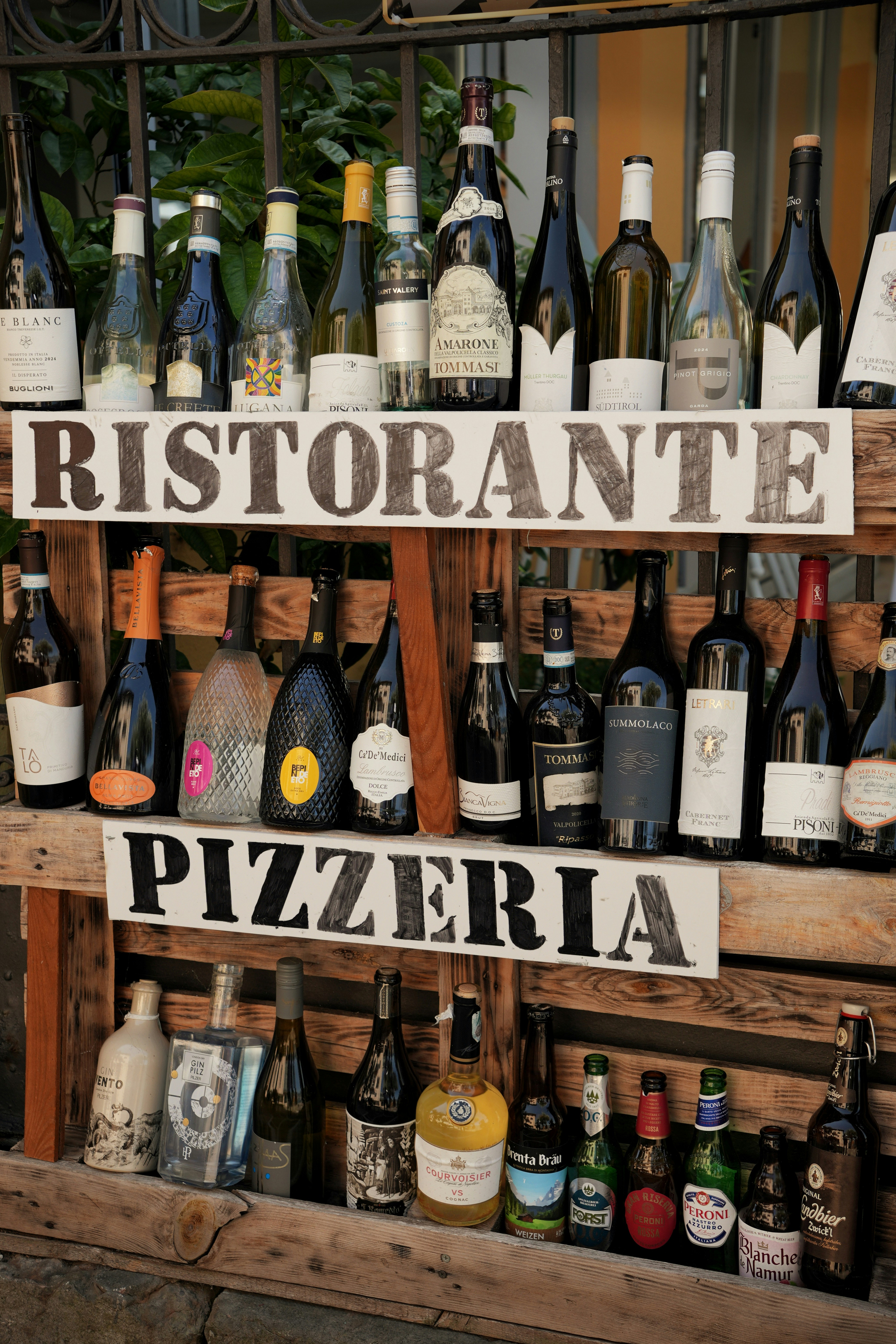 Rows of wine bottles arranged on wooden racks beneath bold signage that reads RISTORANTE PIZZERIA, evoking a rustic Italian eatery ambiance.