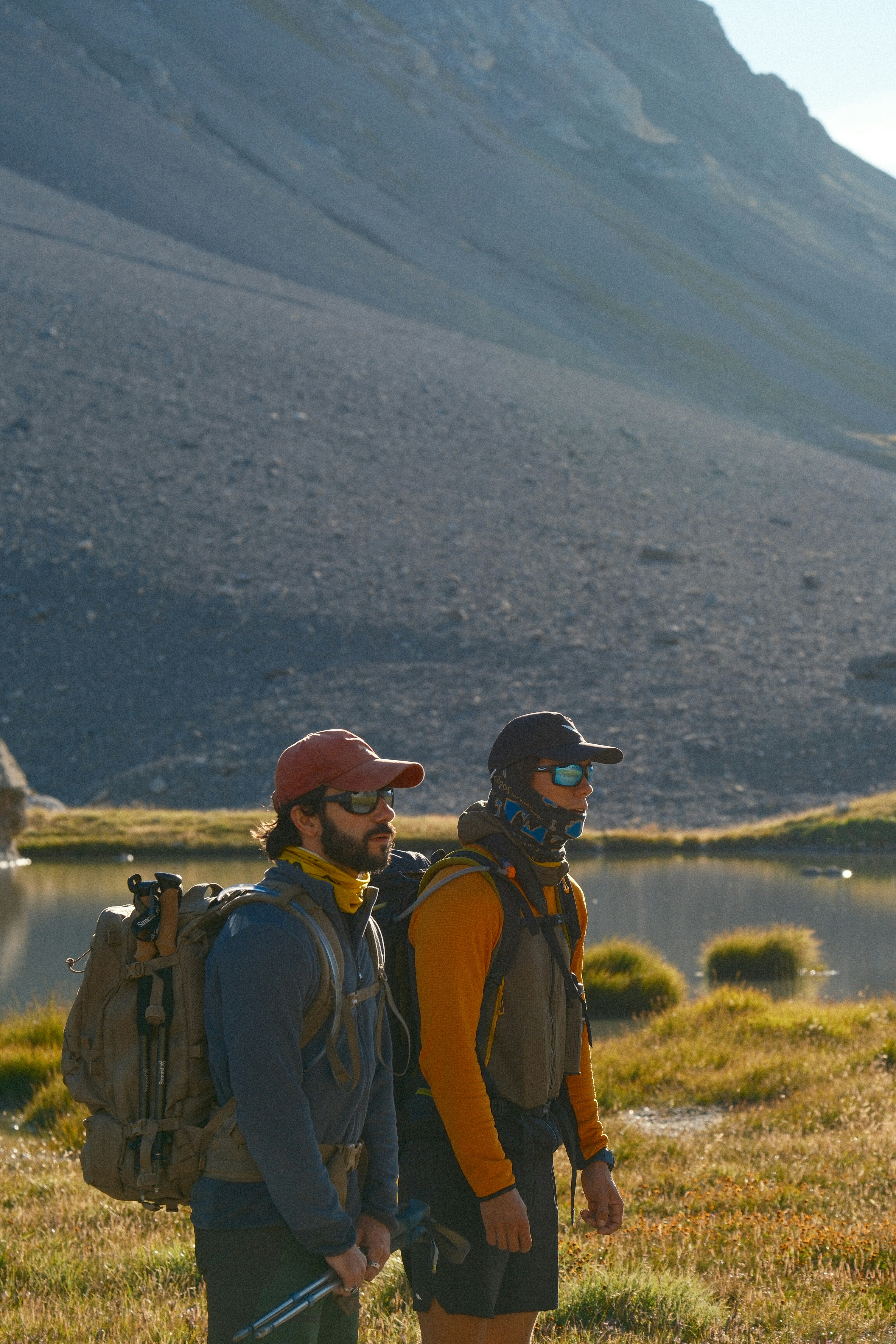 Two hikers at a highland lake under shadowed mountain slopes