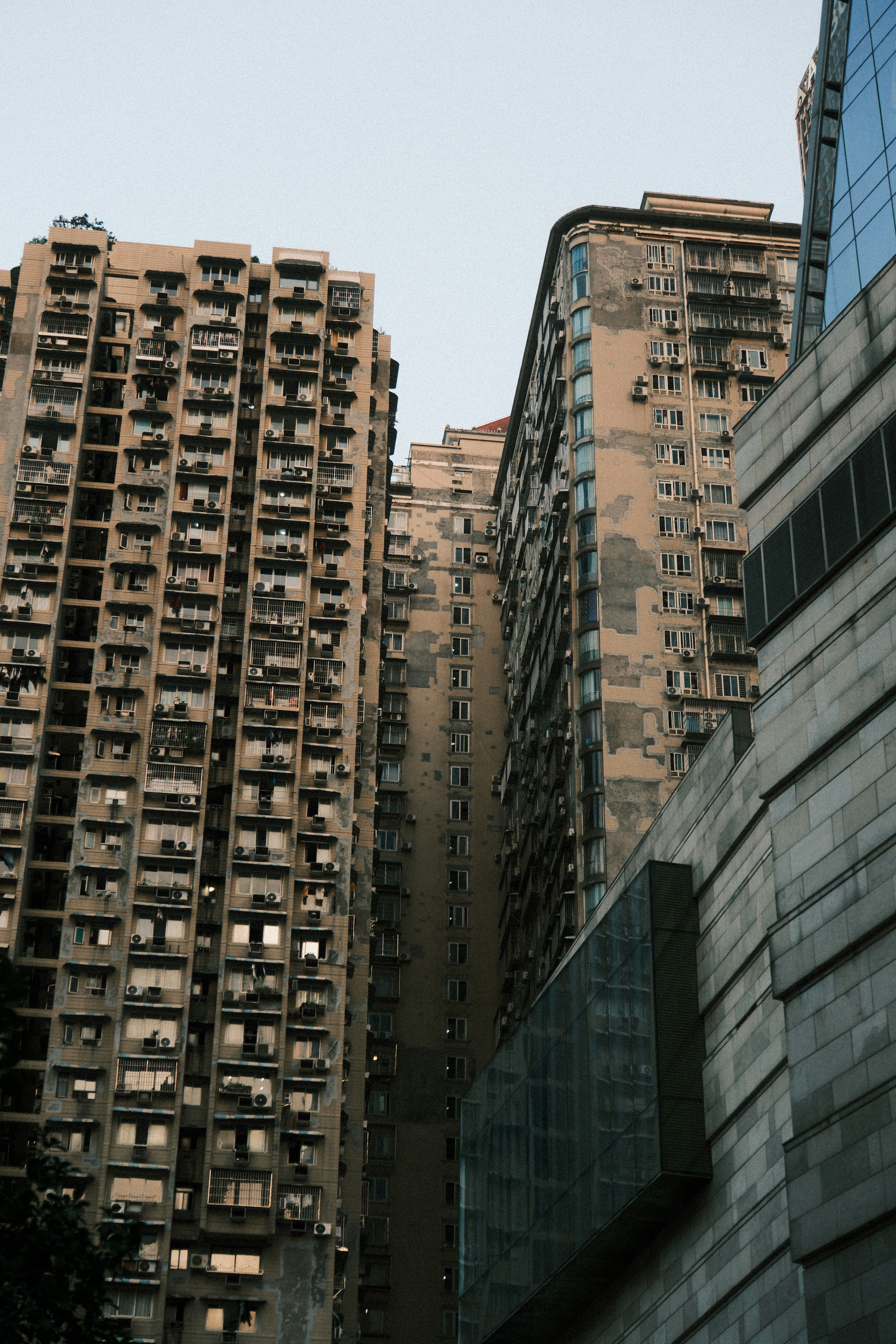 Tall apartment buildings loom in a narrow city canyon with a modern glass structure at the right; the image emphasizes architectural repetition and texture.