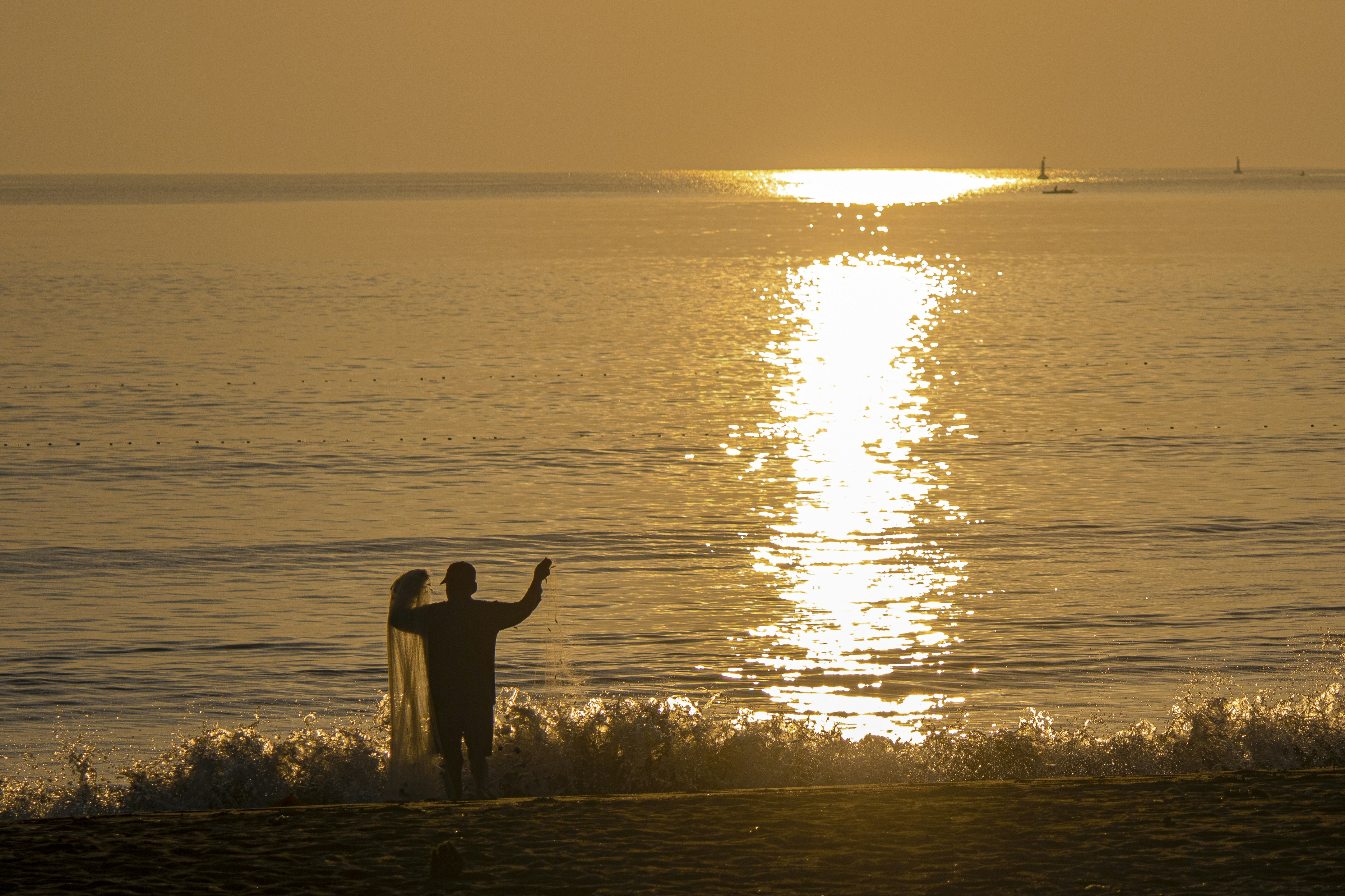 Sunlit Silhouette: Two Figures Amid Gentle Waves at Dusk