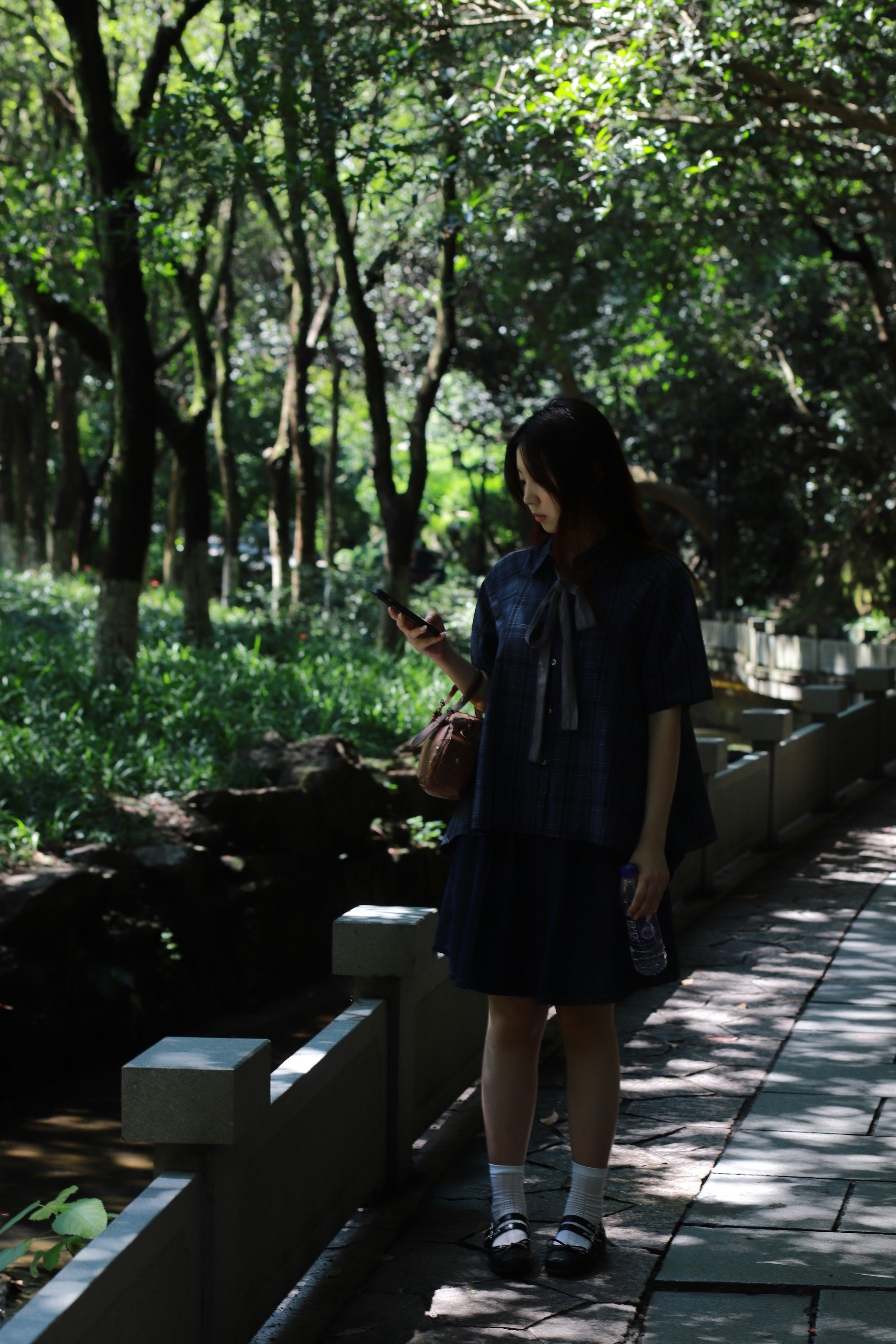 Portrait in Shade: A Young Woman with Phone on a Dappled Woodland Path