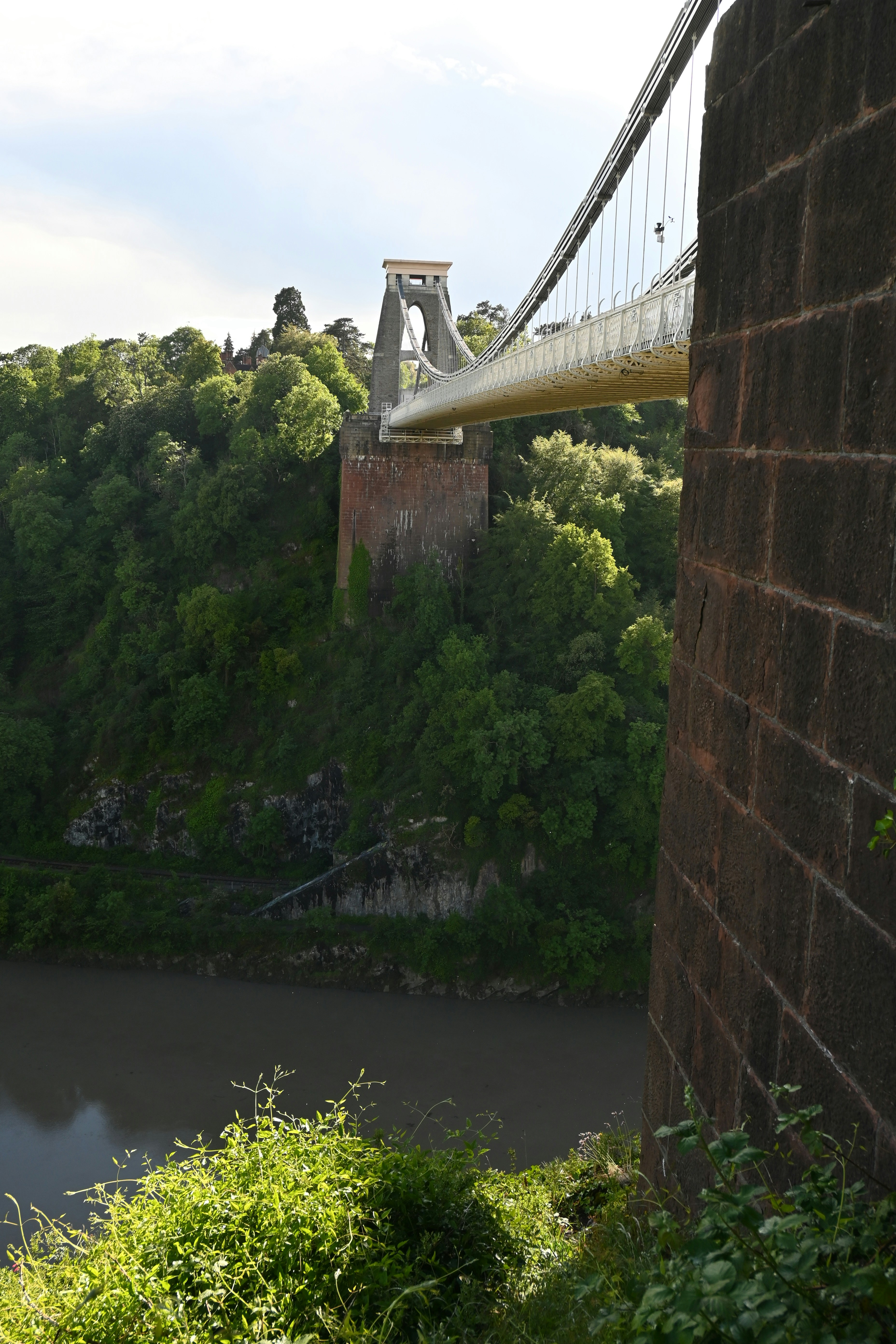 Bridge spans a lush gorge above a calm river; stone abutments loom from the edge while greenery fills the valley. A vantage shot captures the structure and surrounding landscape.