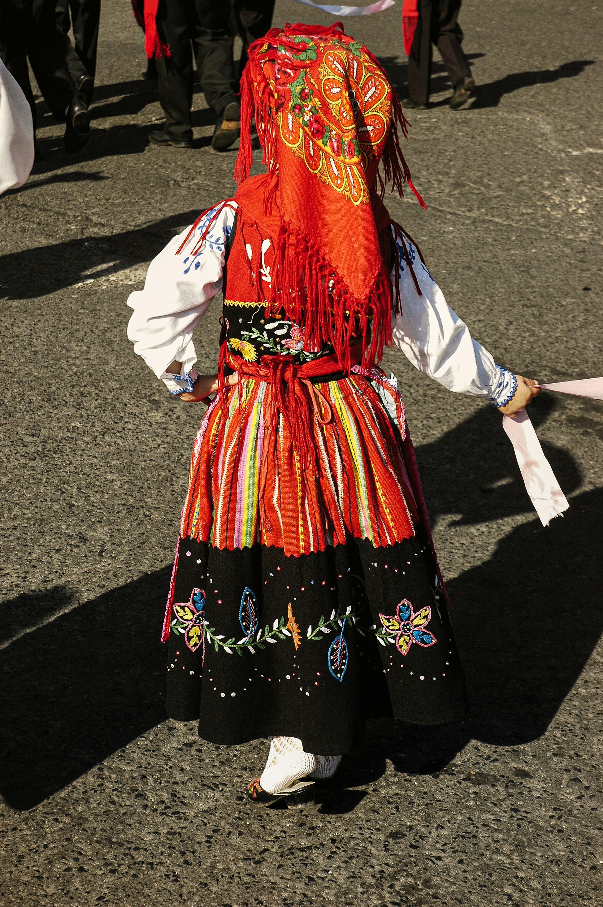 On a sunlit street in Portugal, a figure dressed in vibrant traditional attire becomes the kind of moment travellers remember long after their journey ends. The rich red headscarf, the embroidered blouse and the layered apron move with a quiet grace, echoing centuries of rural craftsmanship and festive ritual. Each colour, each stitch, feels like a fragment of living heritage — a reminder that culture here is not staged, but worn proudly in everyday celebrations. For visitors seeking authenticity wrapped in beauty, this scene offers a rare glimpse into Portugal’s soulful traditions, where community, artistry and identity come together in a way that feels both timeless and deeply human.