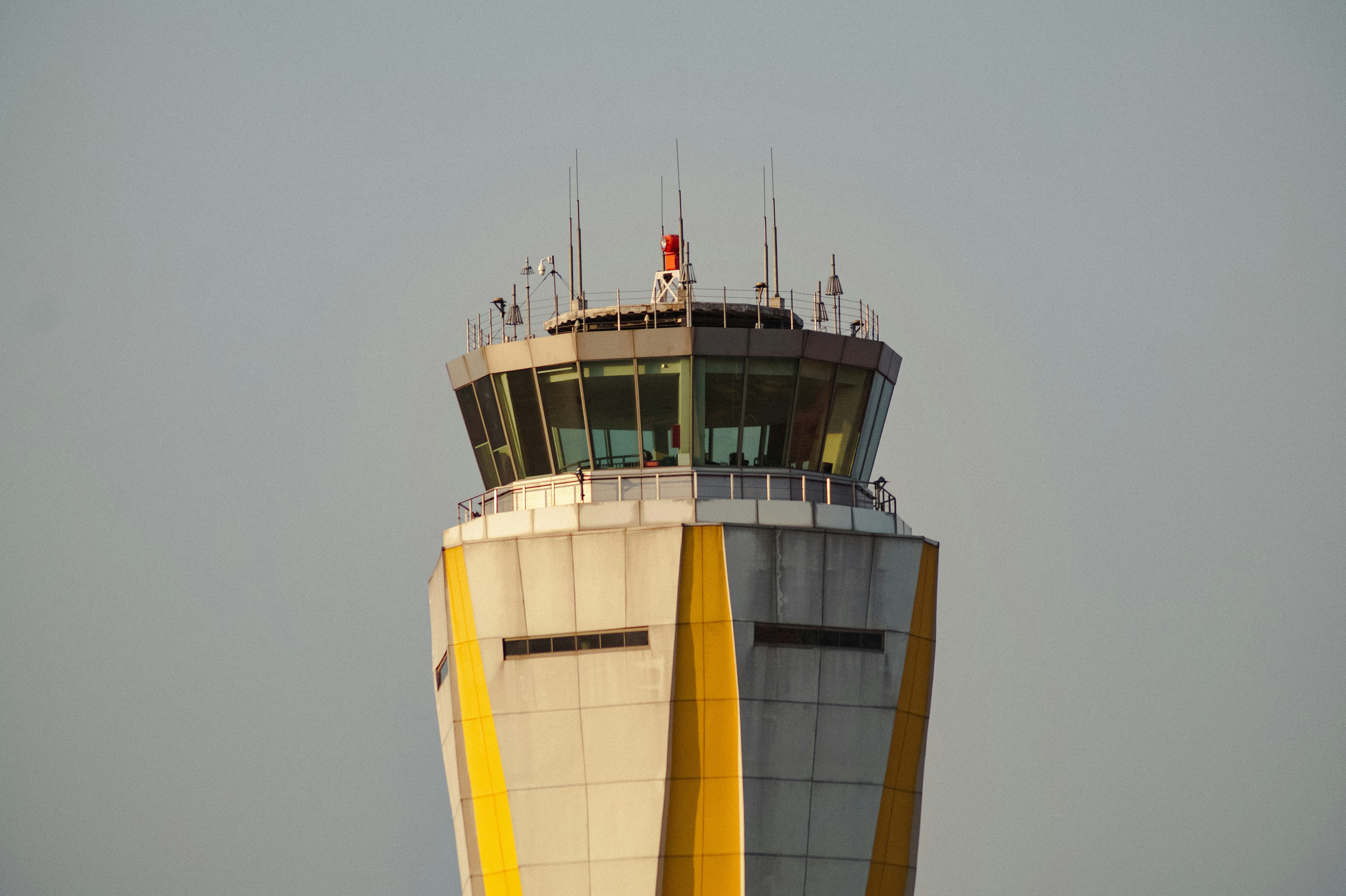 Air traffic control tower rises with bold yellow accents against a pale sky, highlighting its commanding presence and top observation deck.