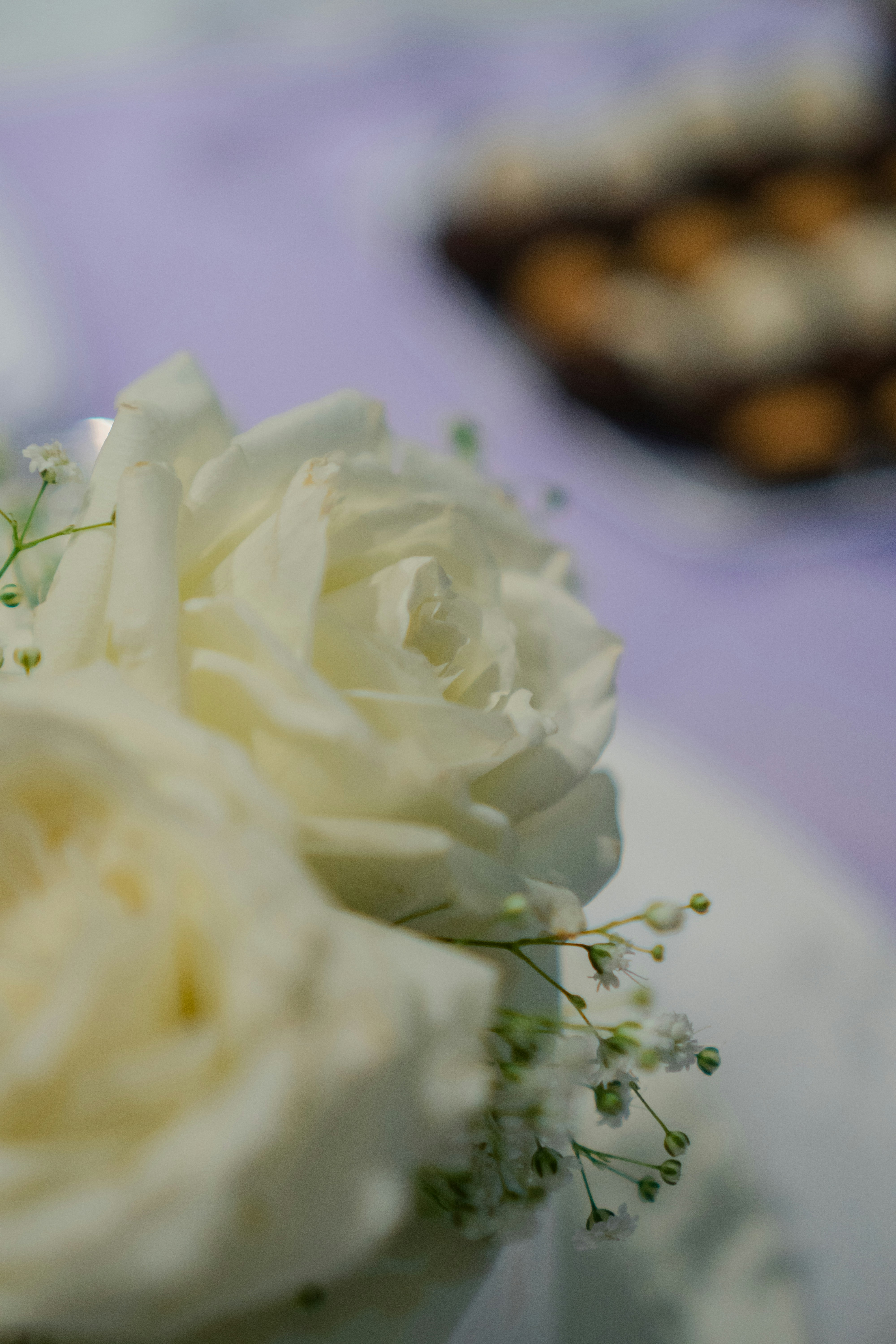 White roses dominate the foreground with delicate petals; a blurred dessert table is visible in the background, suggesting a wedding or special occasion setup.