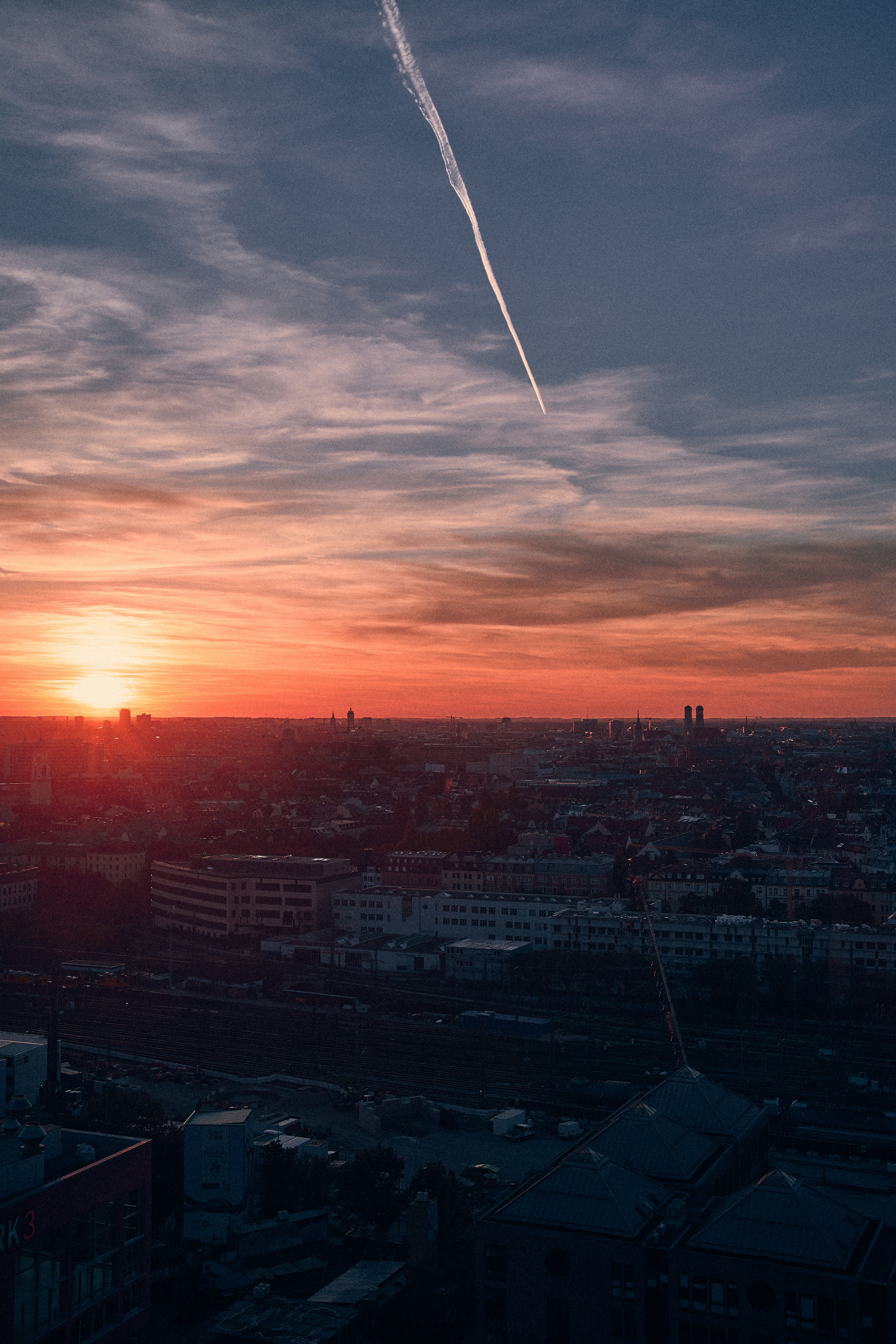 Sunset over the city: contrail arc cutting a warm horizon