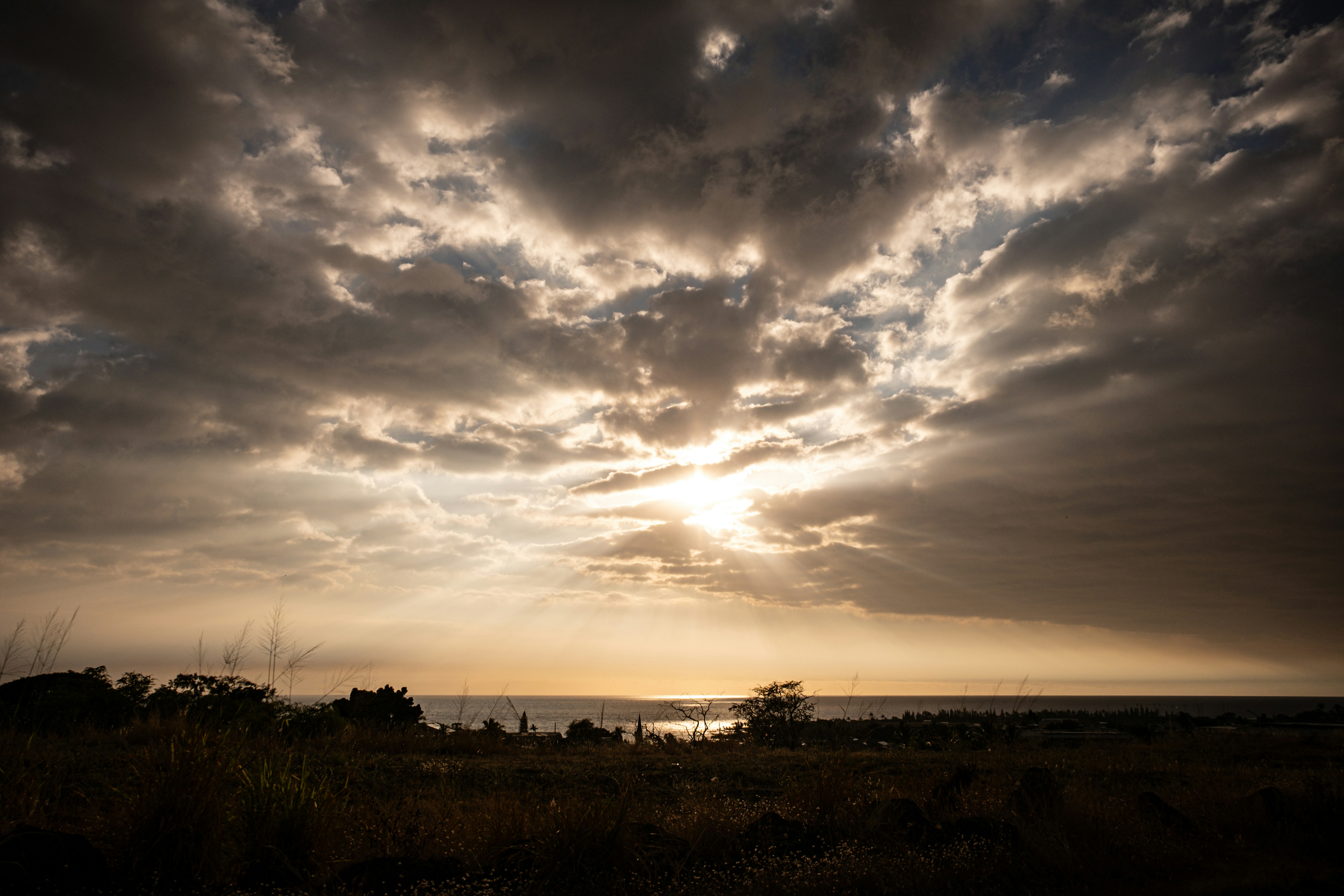 Horizon Fire: Sun Piercing Clouds Over a Quiet Shore