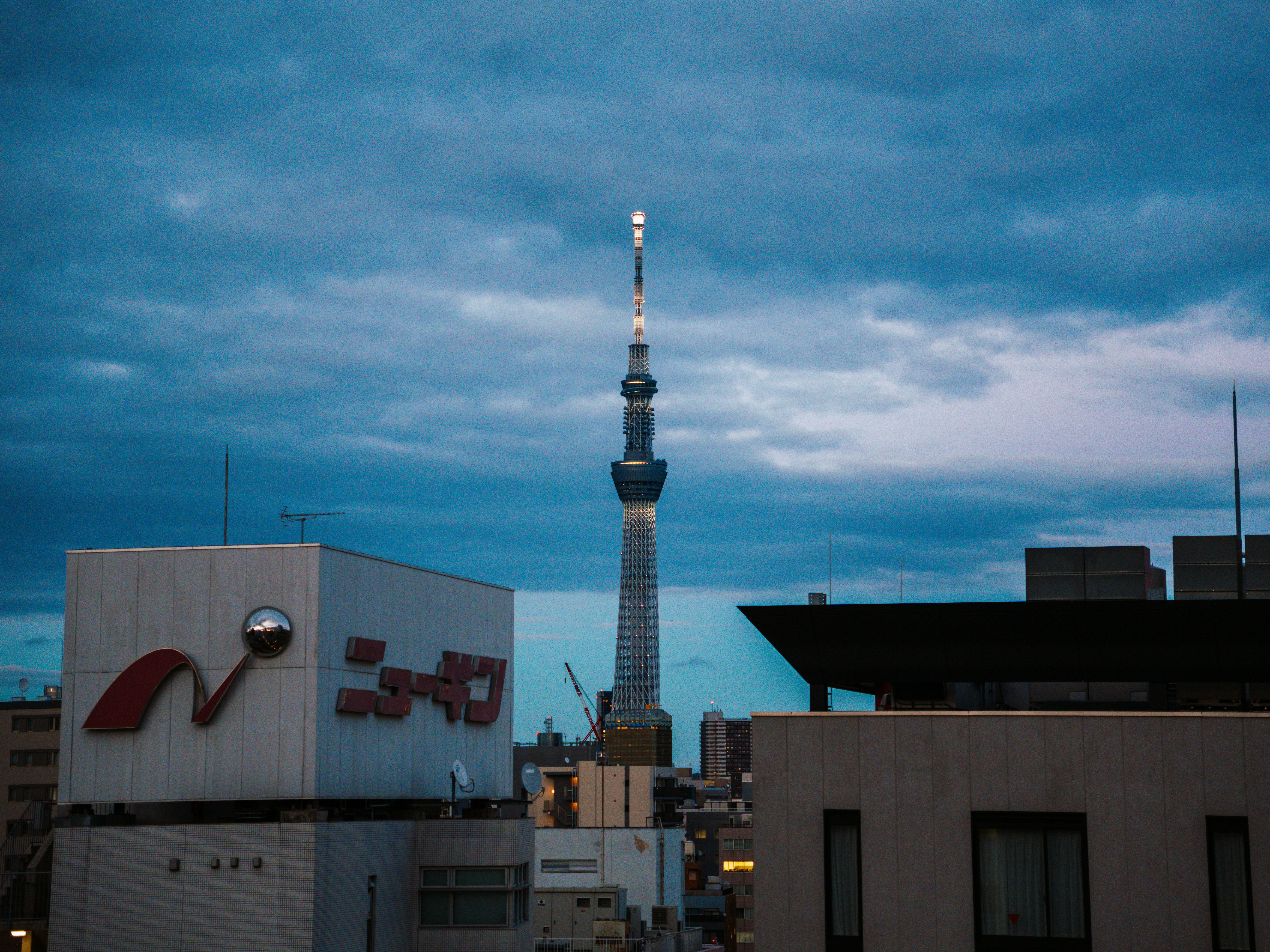 Urban skyline with a tall tower rising above low clouds behind a cluster of modern buildings.