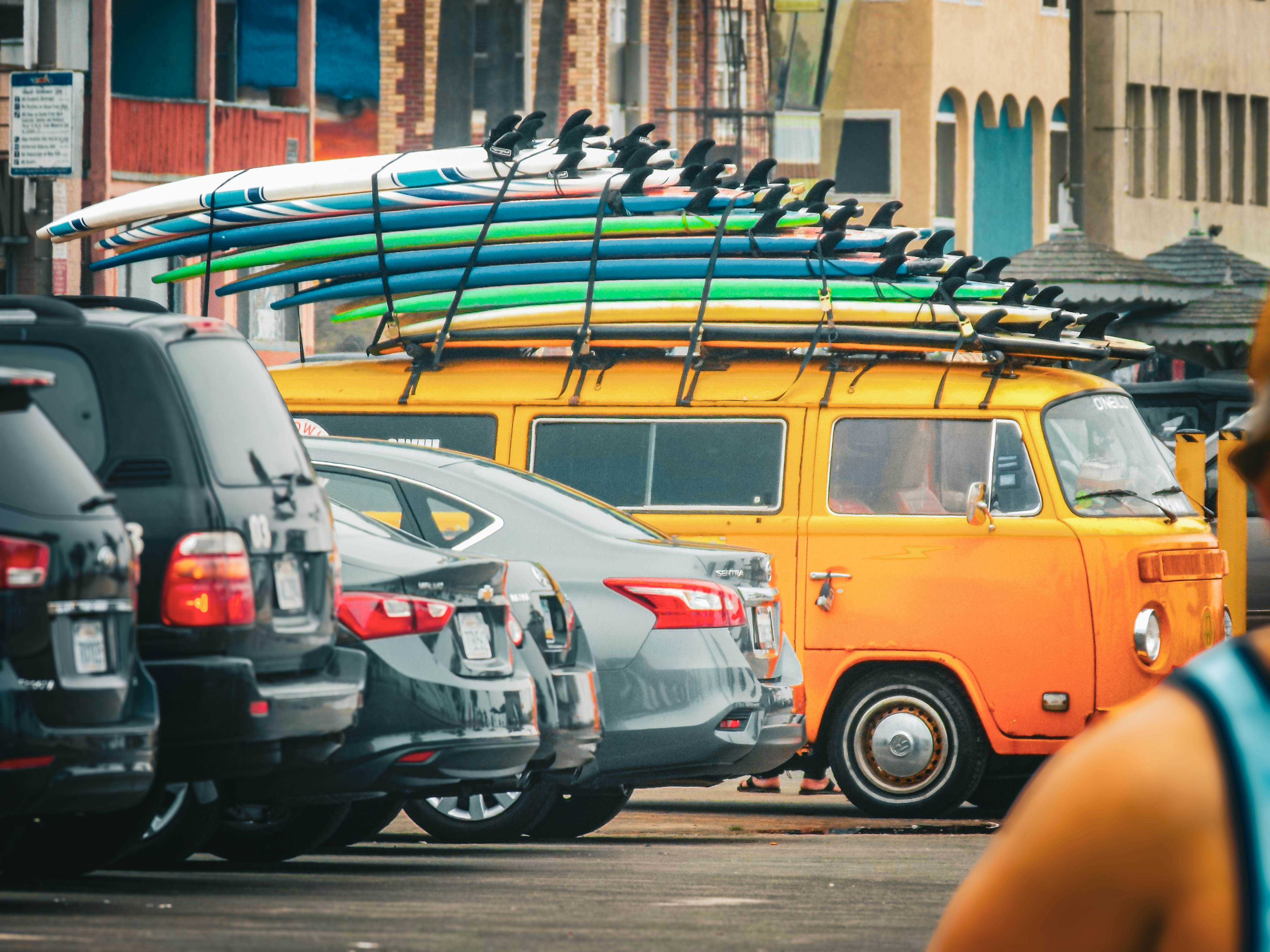 Sunlit Orange Van with Surf Racks in a Colorful Parking Lot