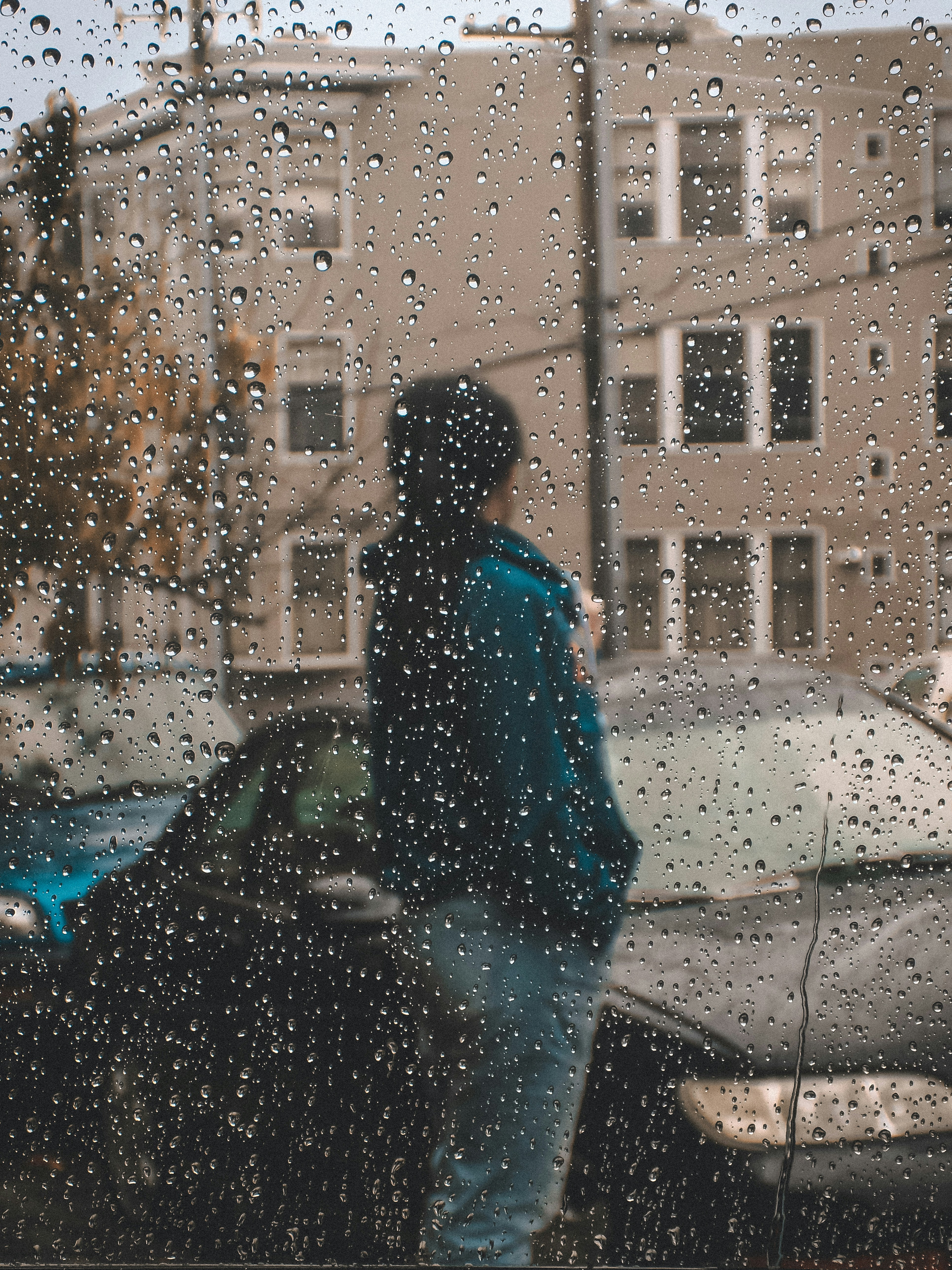 Rain-kissed silhouette: a figure in a teal jacket amid a glass-dotted storefront