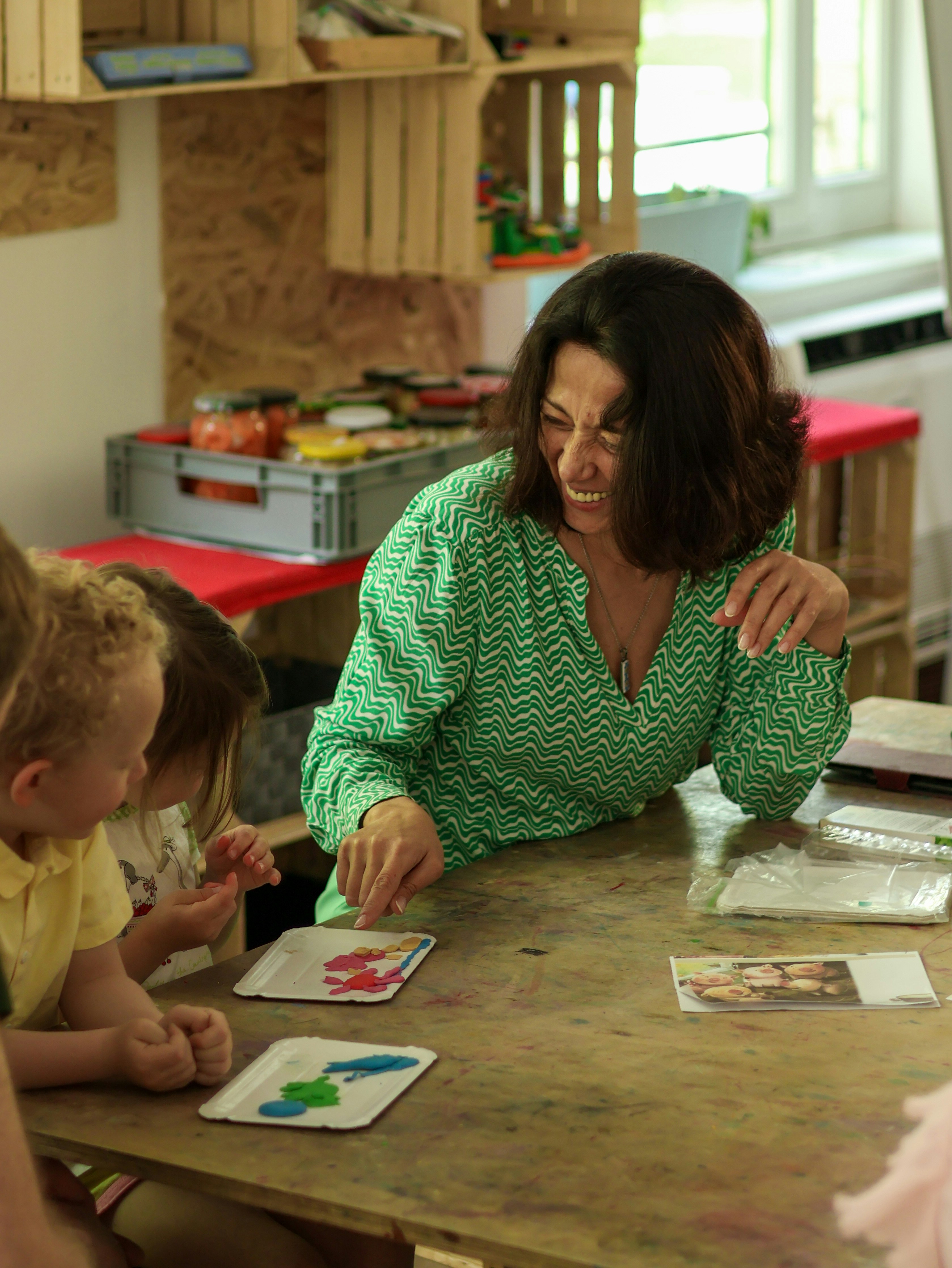 Teacher at a sunny crafting table laughing with children