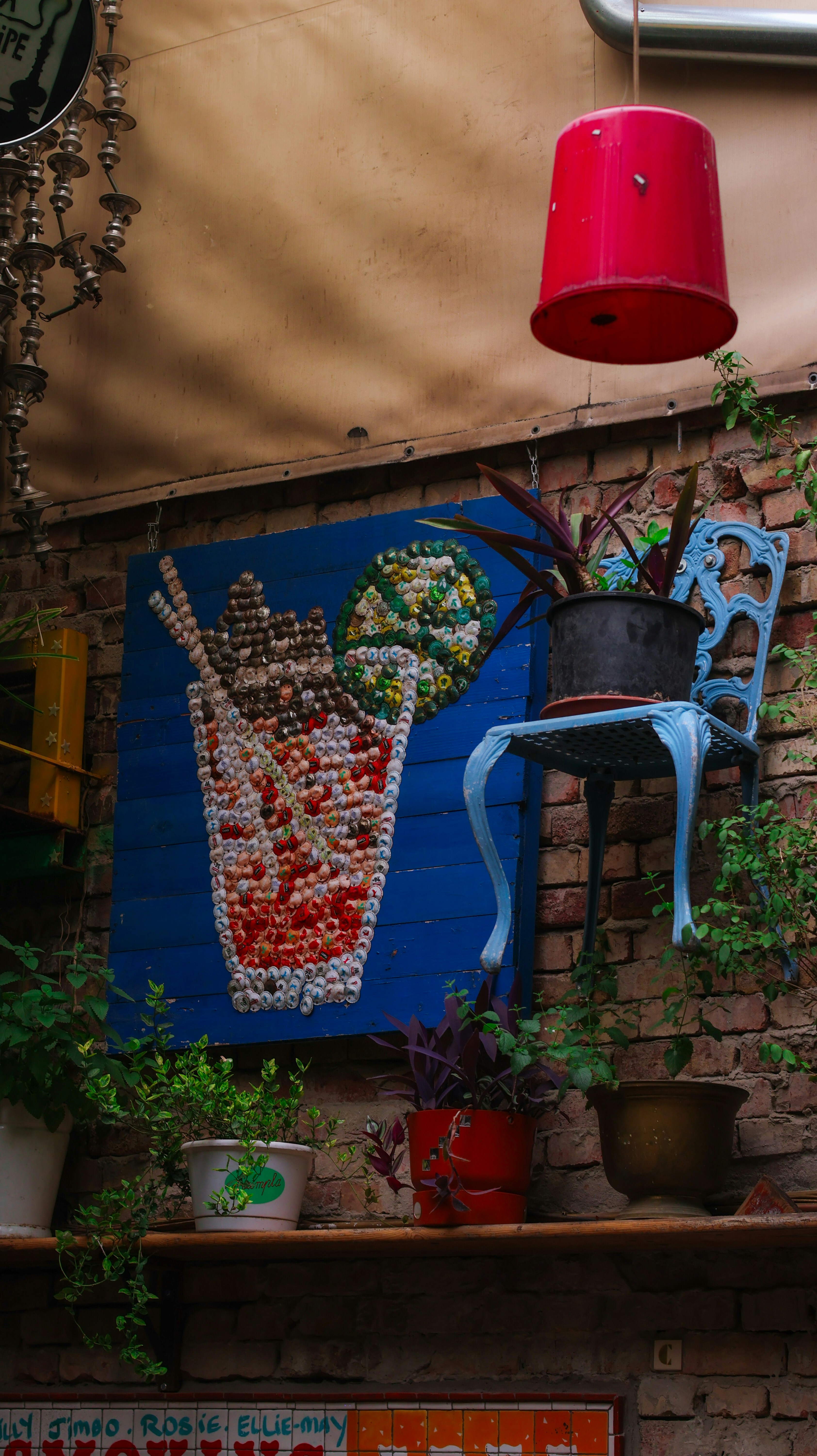 An urban vignette: a neon-red lampshade above a brick wall with a quirky mural and potted greenery