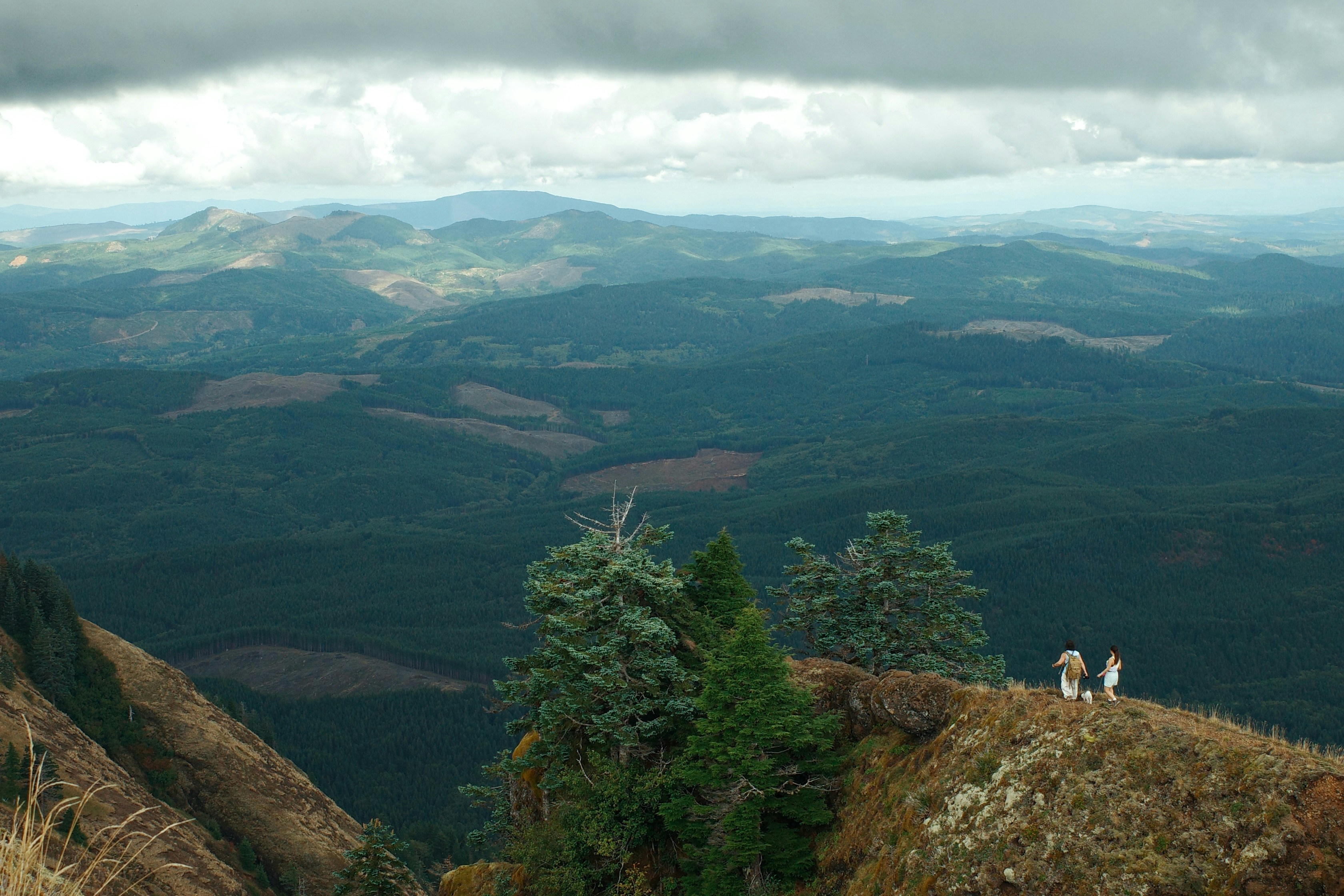 Two hikers at the edge: a panorama of distant ridges from a cliff