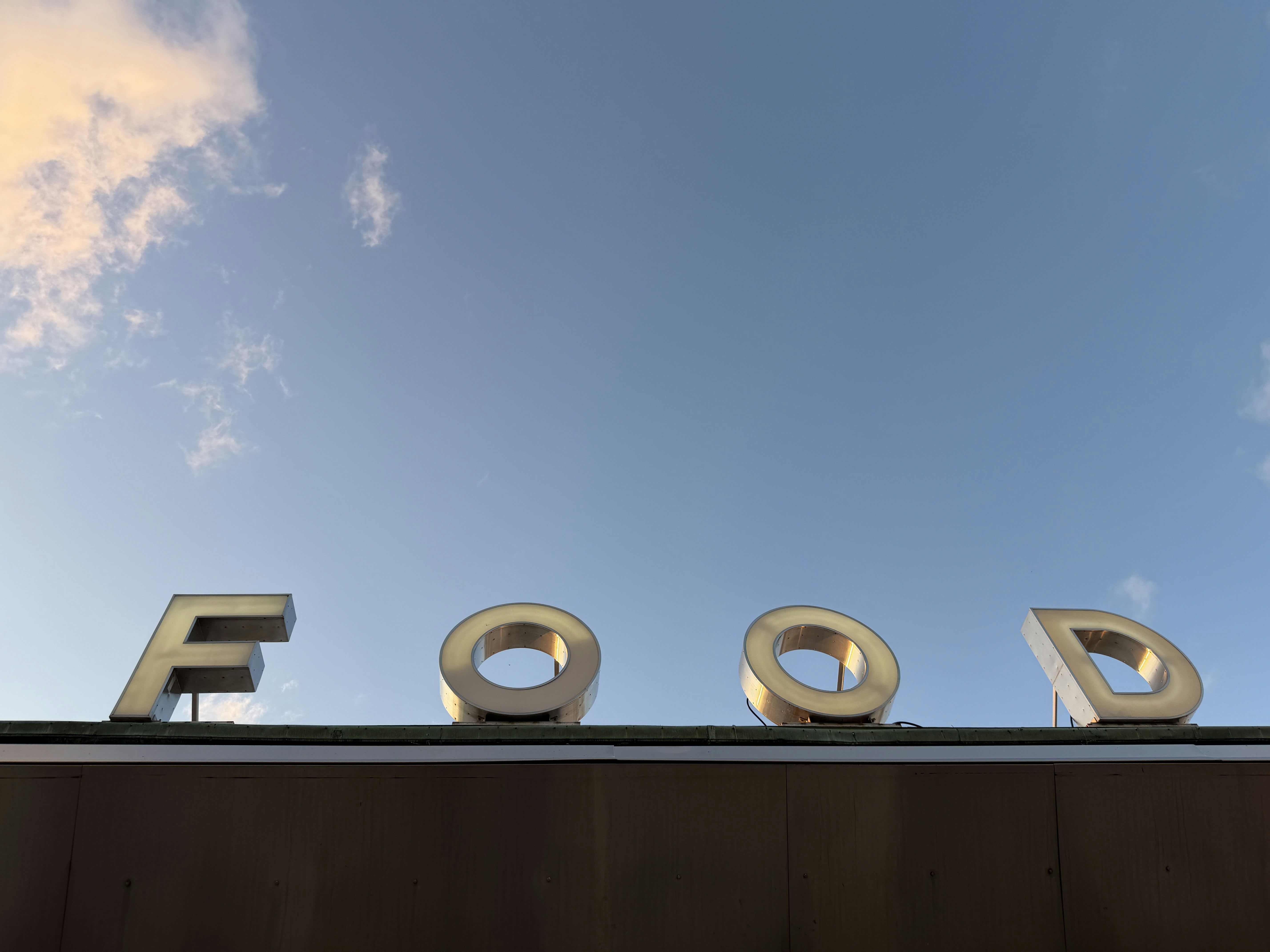 Neon Sign on a Quiet Rooftop: The Rising Letters Against a Clear Sky
