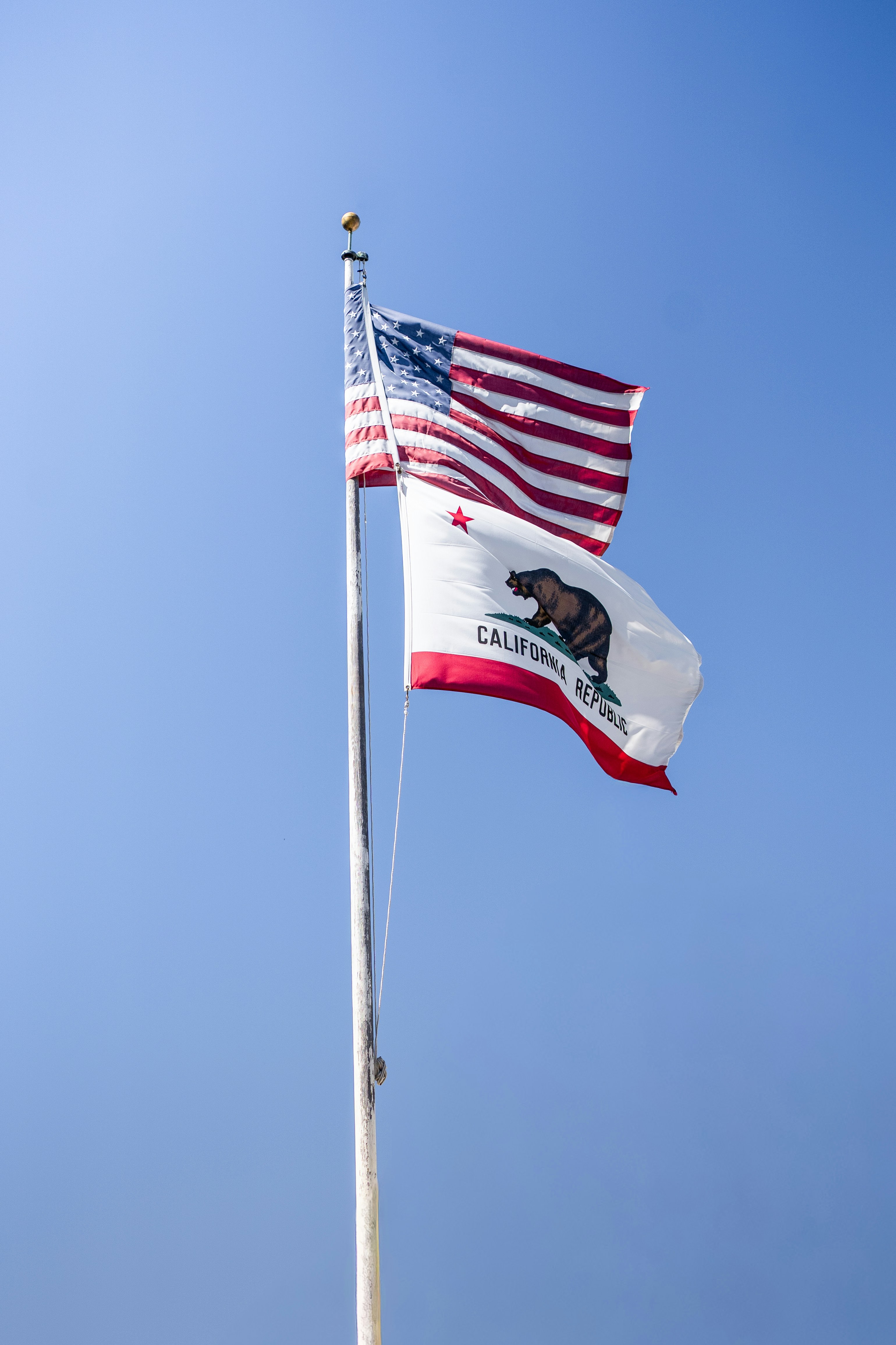 Flagpole orbits: American and California banners in a clear blue sky