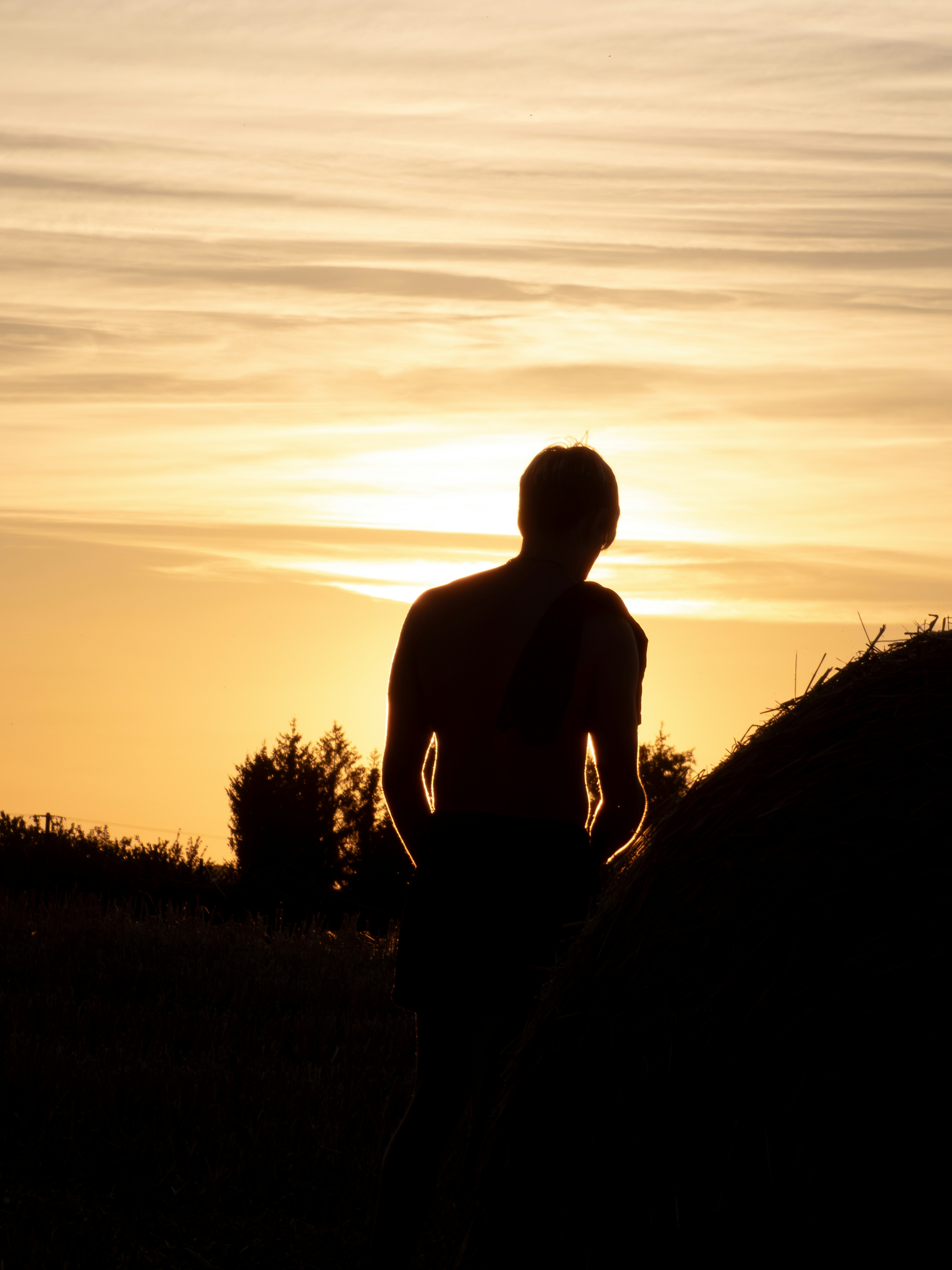 Silhouette at Sunset: A solitary figure beside a haystack against a molten sky