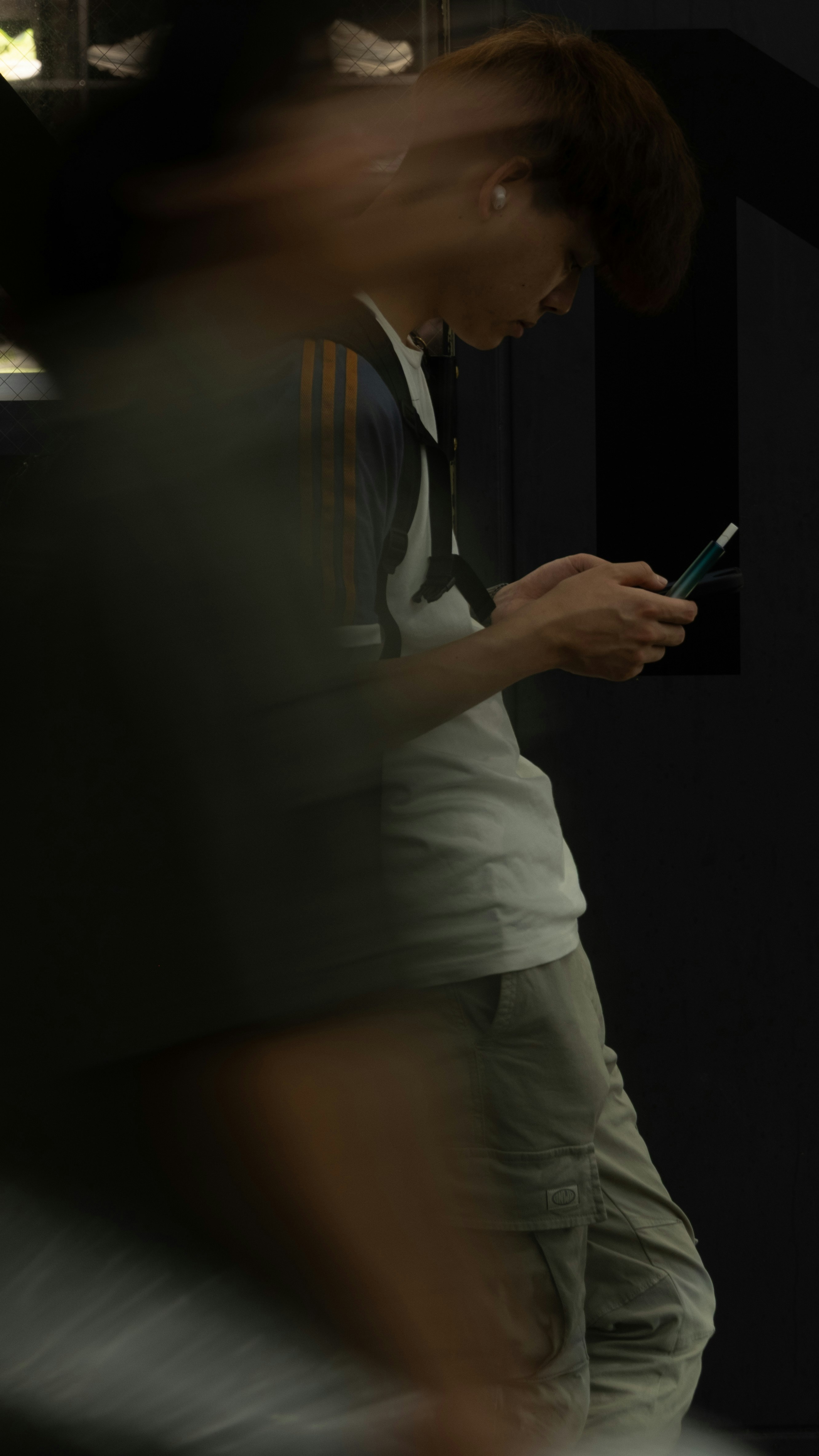 Quiet Focus: A Teen Commutes with a Glance at His Phone in a Dark Corridor