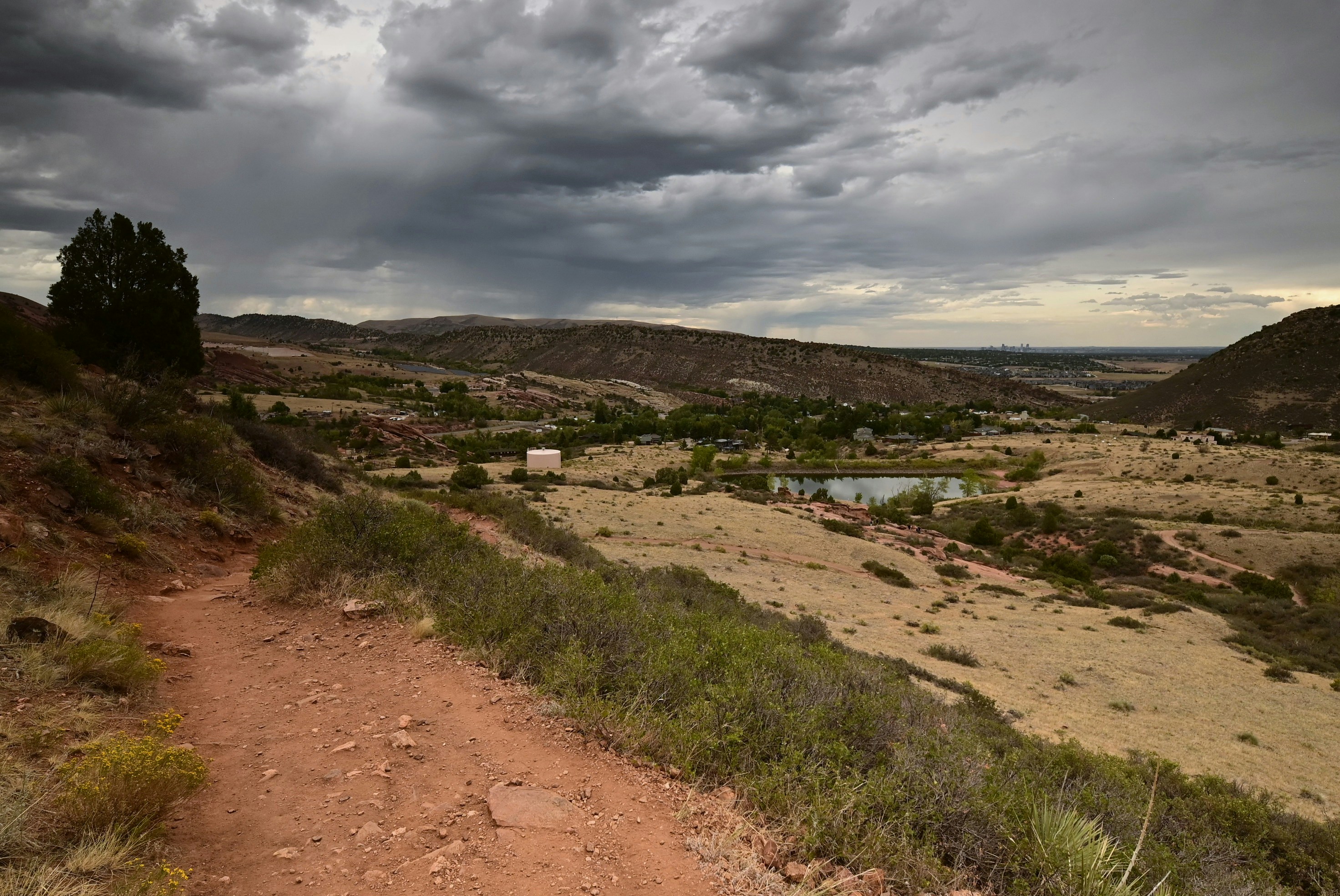 Rugged trail leads into a arid valley with sparse vegetation and distant water, under dramatic sky. A landscape scene captured to emphasize depth and openness; no text or logos present.