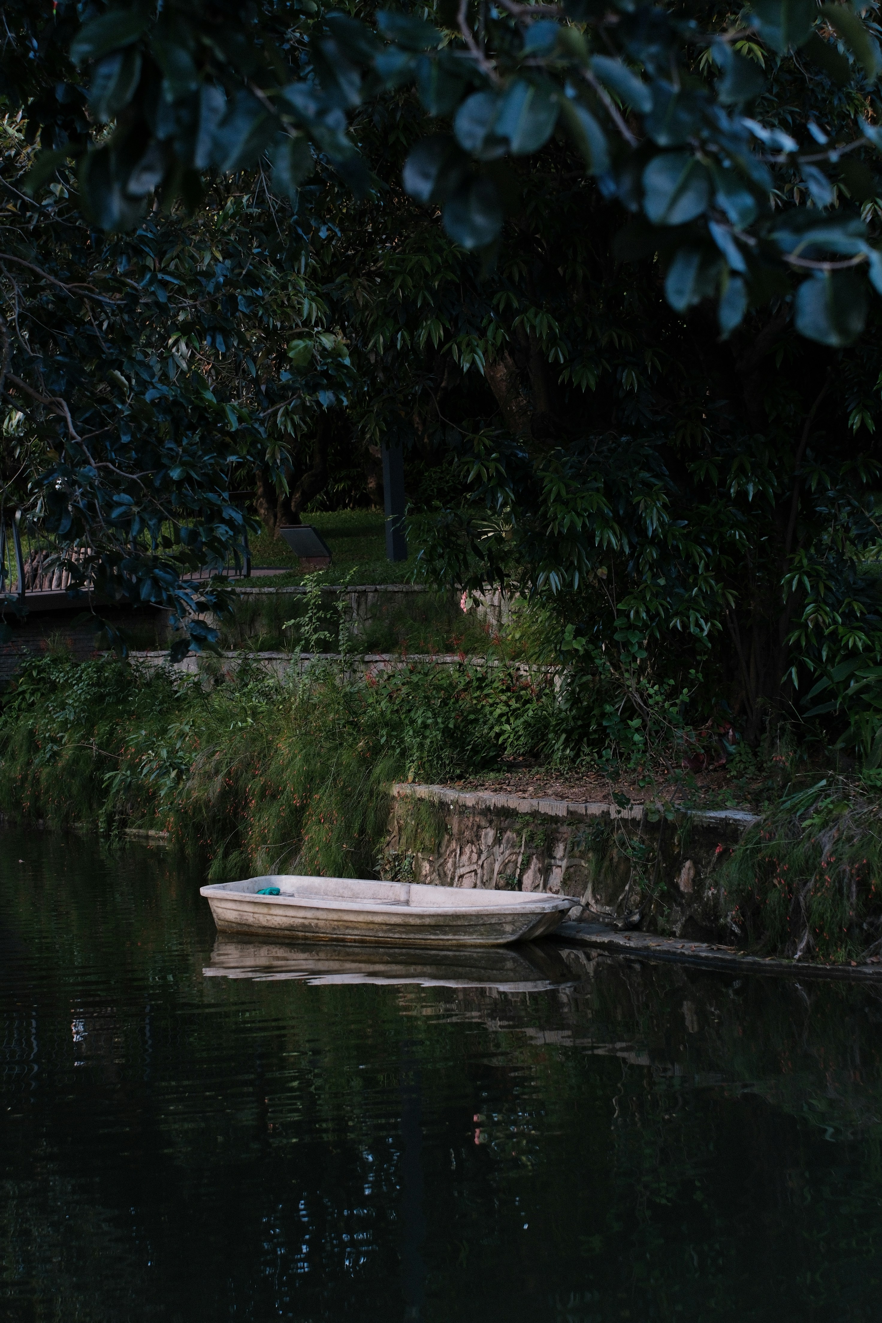 A lone white boat rests along the canal’s edge, framed by dark, overhanging foliage and a calm, reflective water surface.