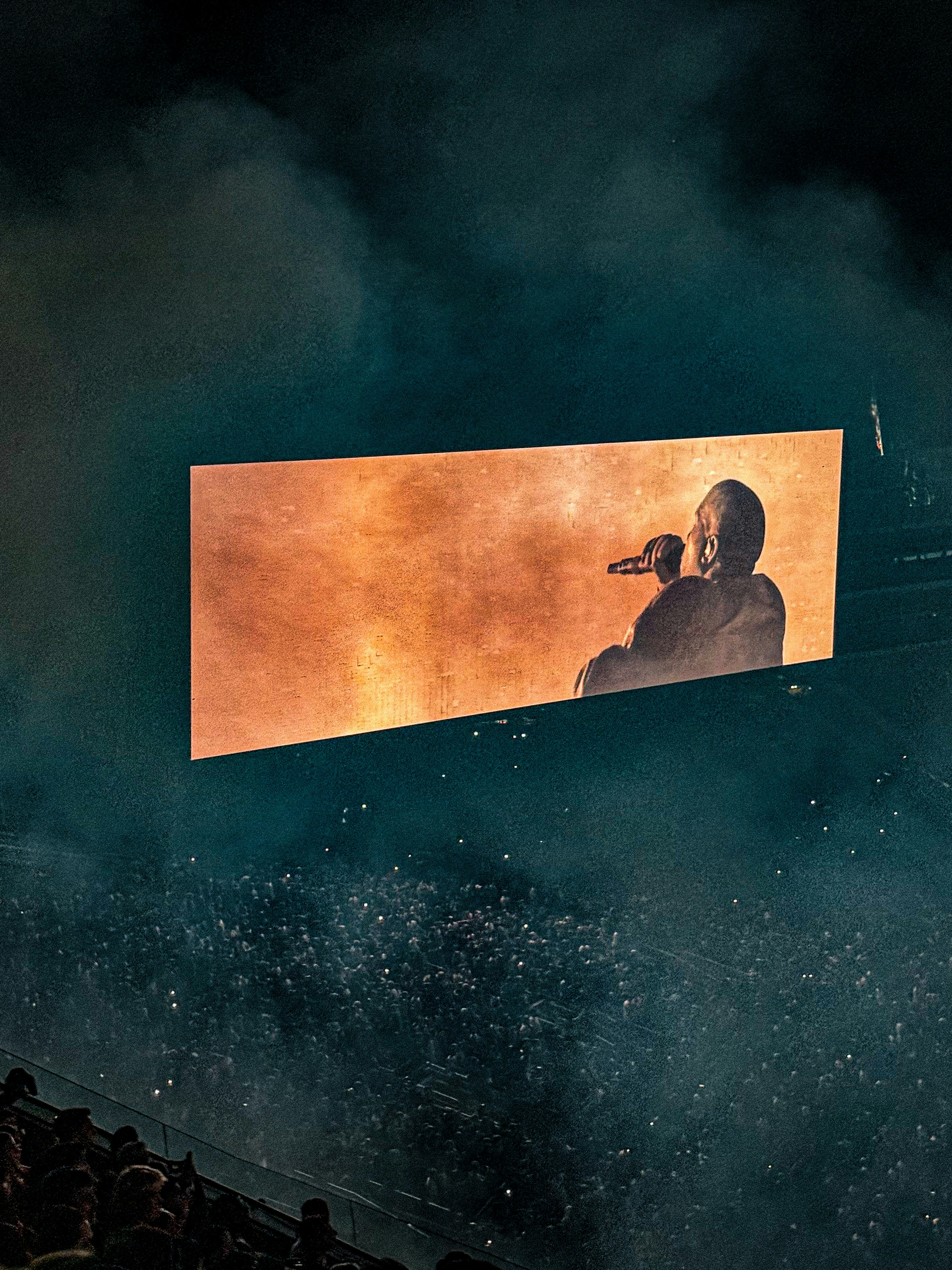Spotlight on a silhouette: A lone performer on a giant screen above a hazy arena