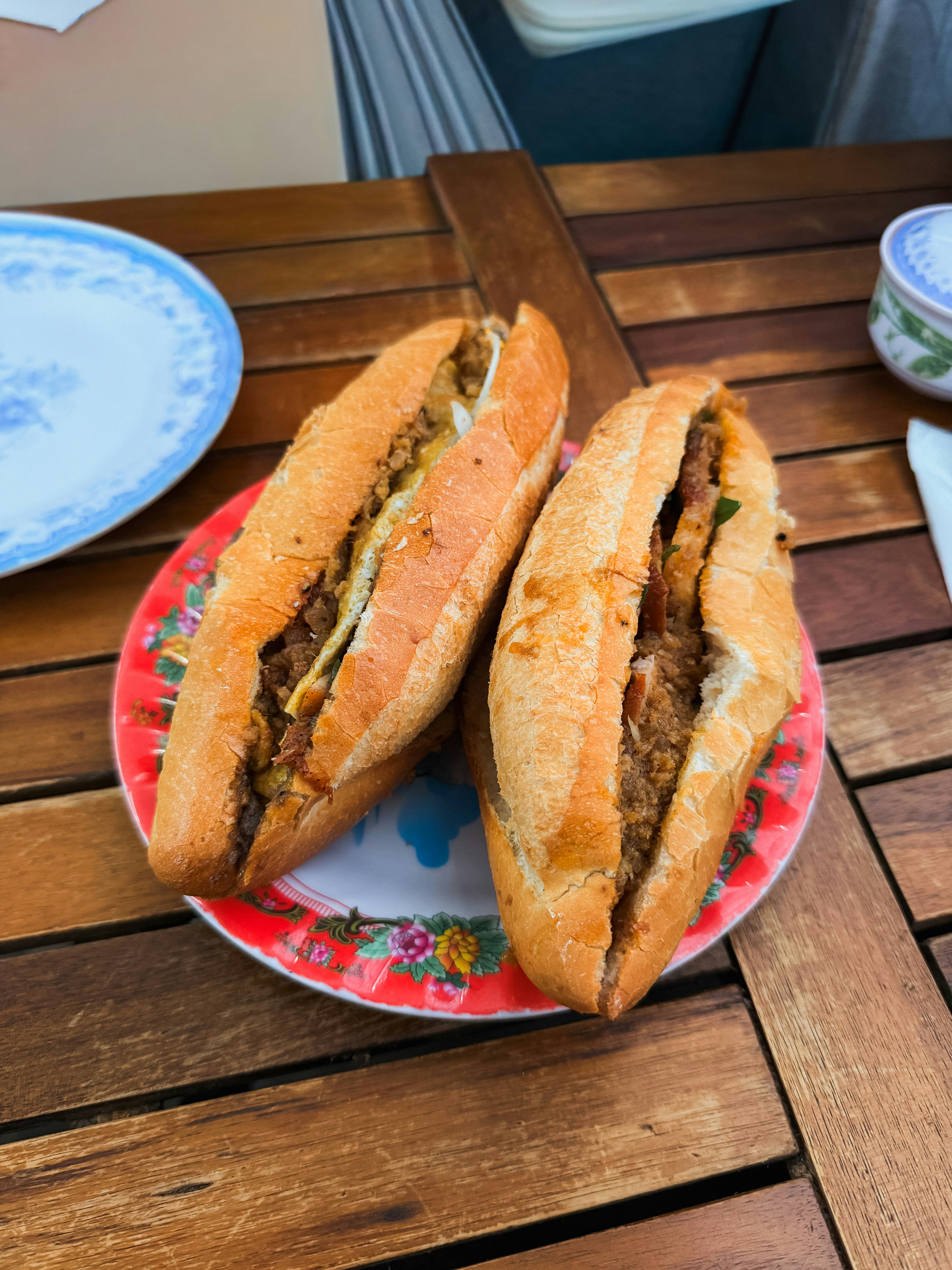 Two loaded banh mi on a floral plate atop a wooden table
