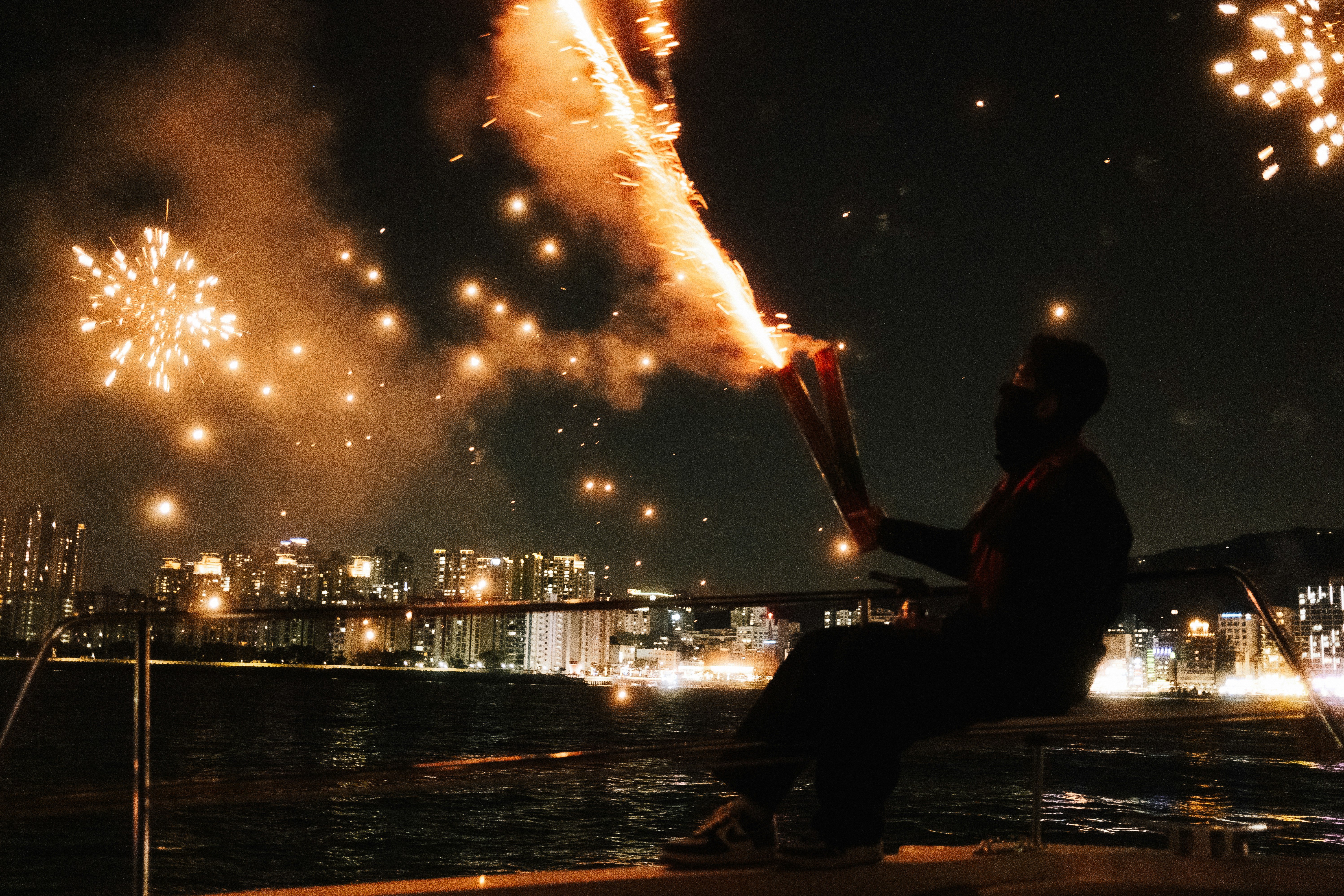 Firework Stroll: A Seated Pyro Performer Against Night City Lights