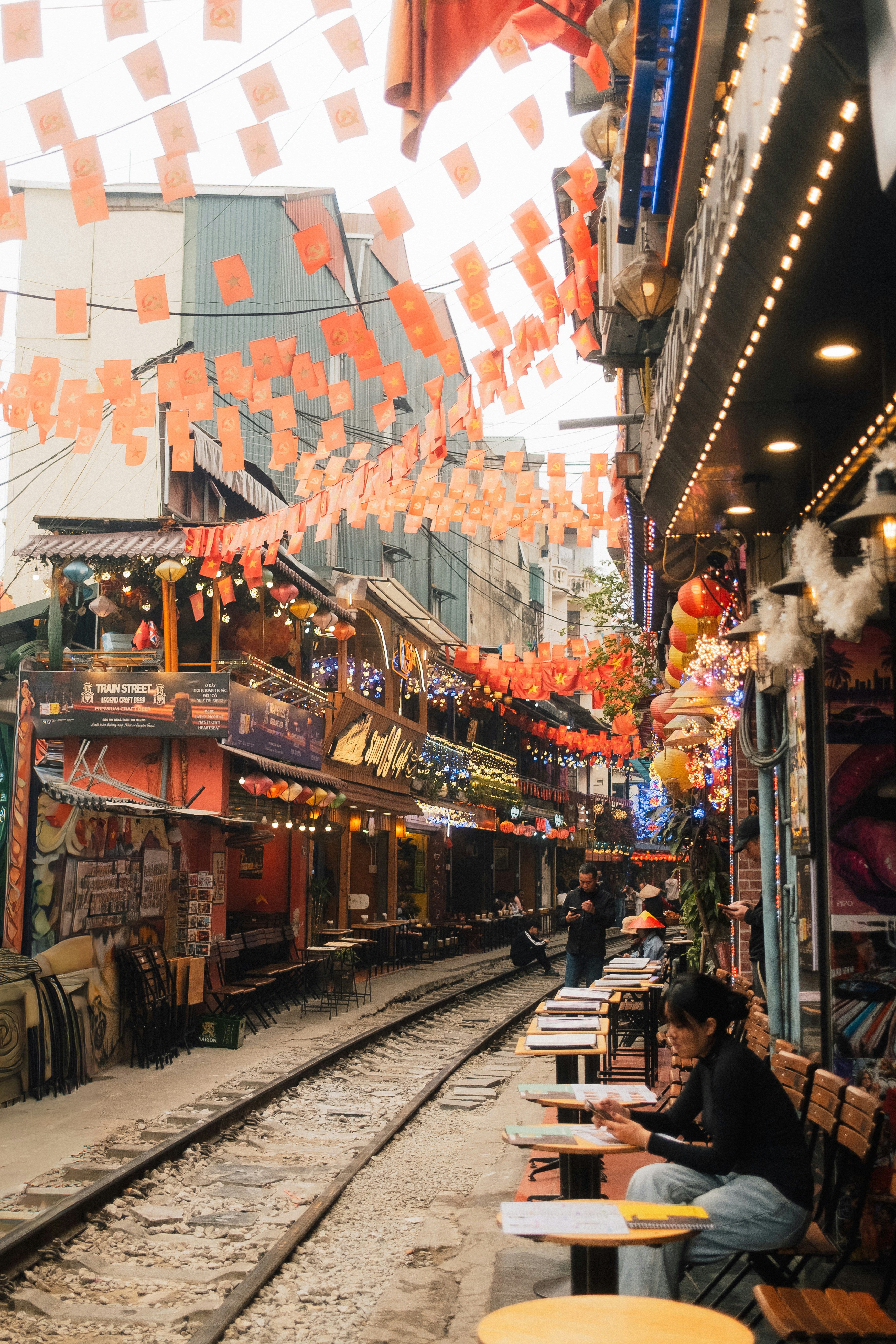 Lantern-lit Lane: A Train-Track Café Scene Under Orange Flags