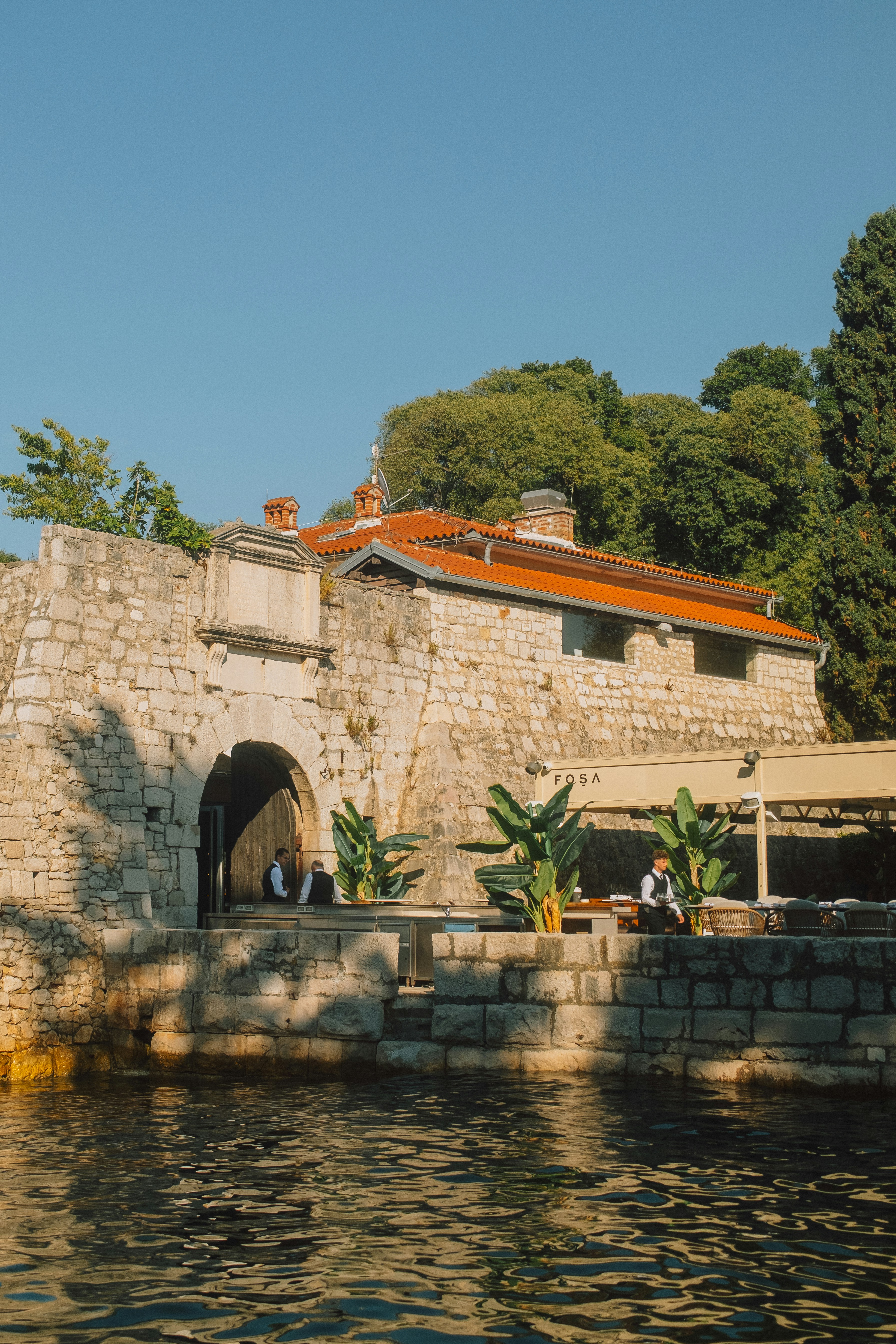 Stone Fortress by the Water: Sunlit Terrace and Red-Tiled Roof
