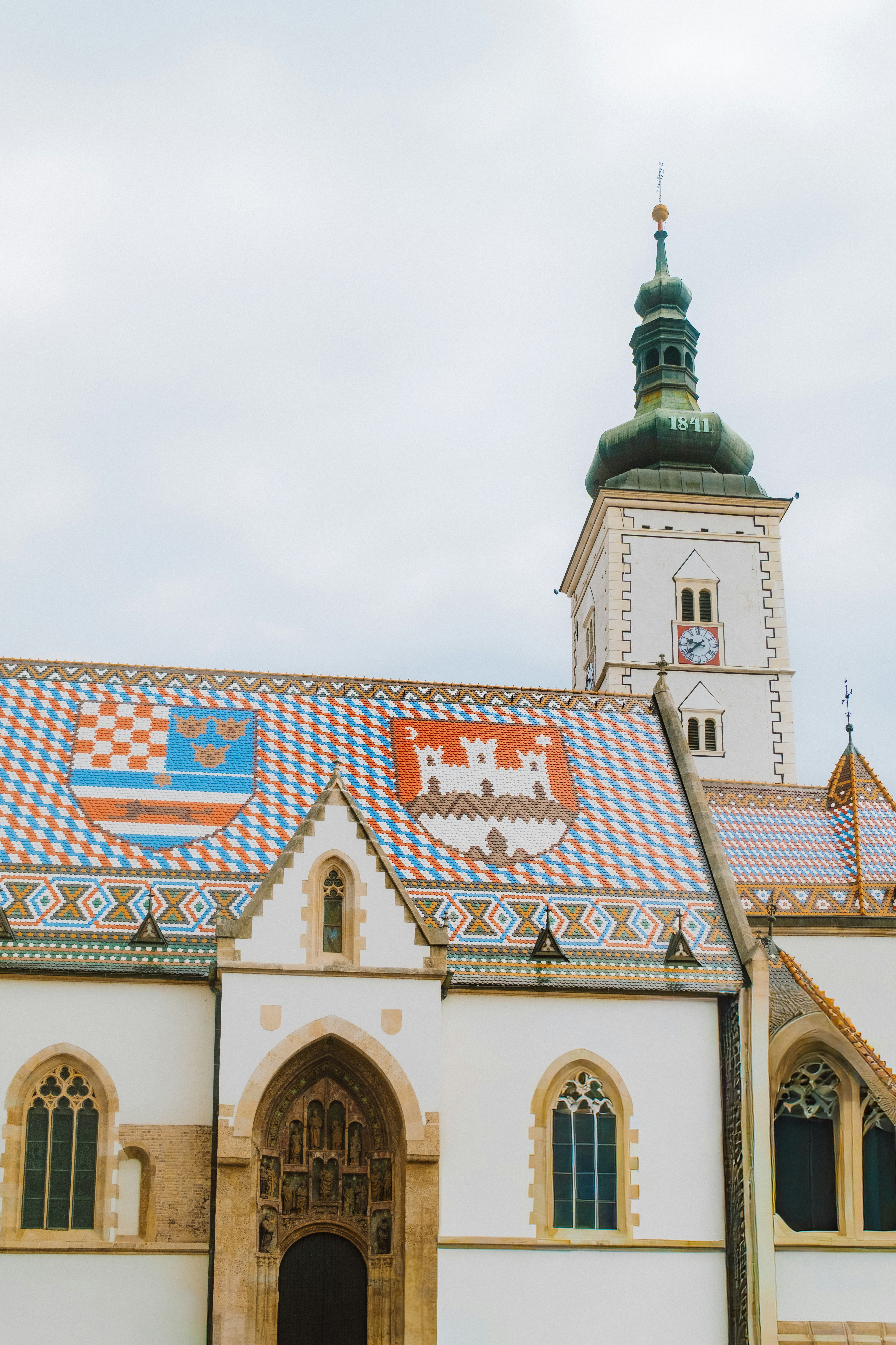  tiled roof of a historic church with clock tower and colorful crest patterns