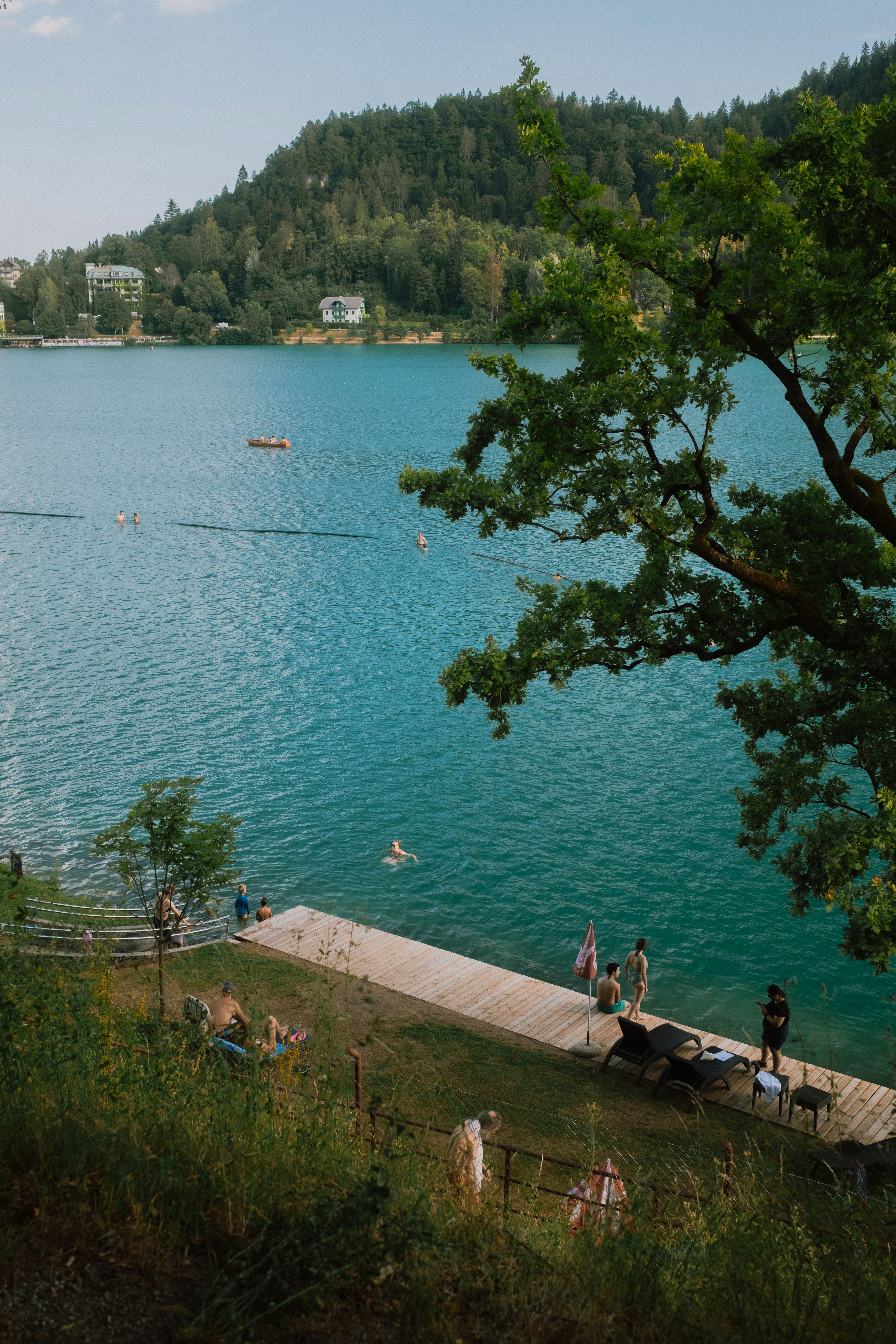 Azure Lakefront: People, Pier, and Dappled Tree Shade