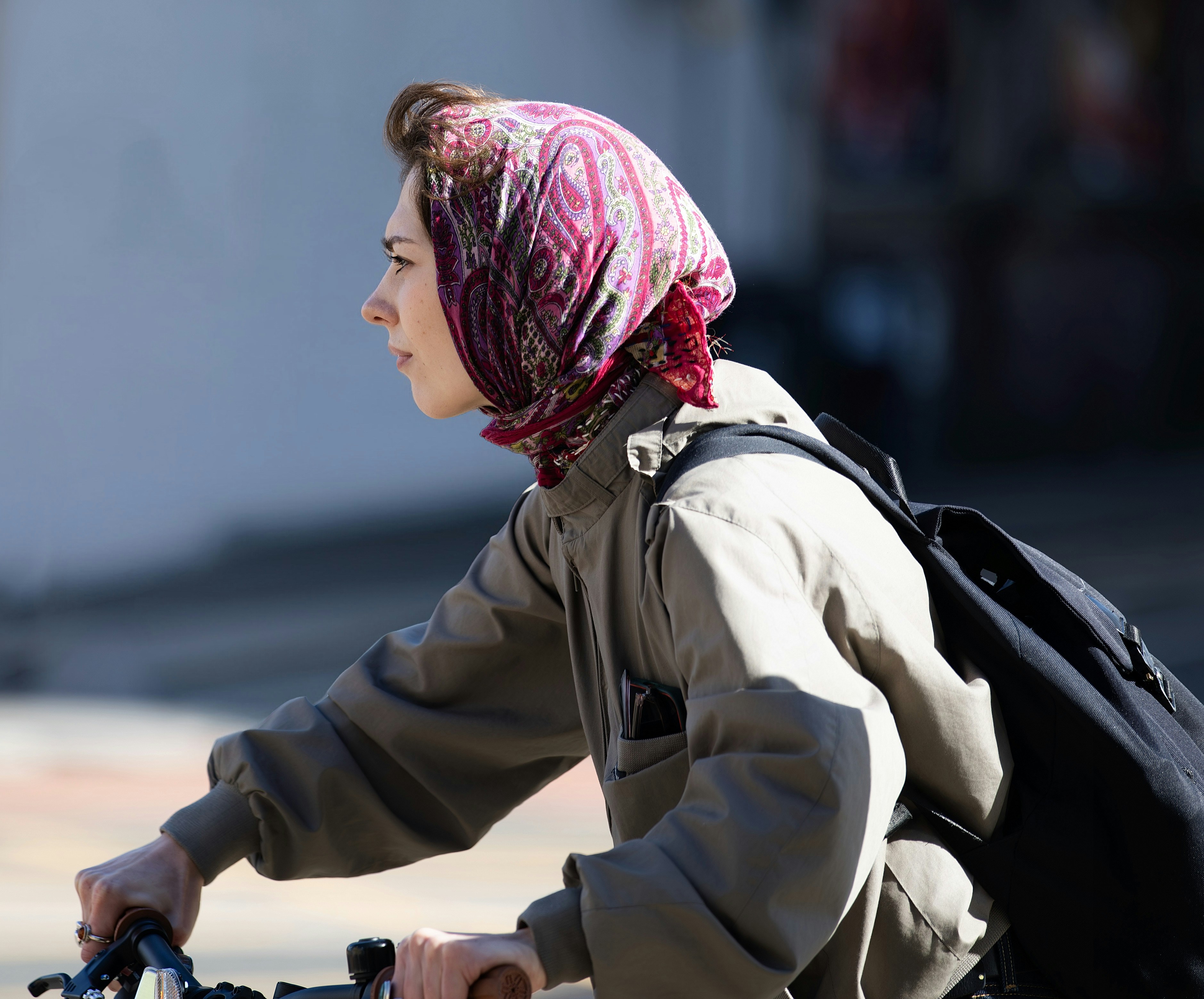  forward motion: a cyclist in a patterned hijab across a sunlit street