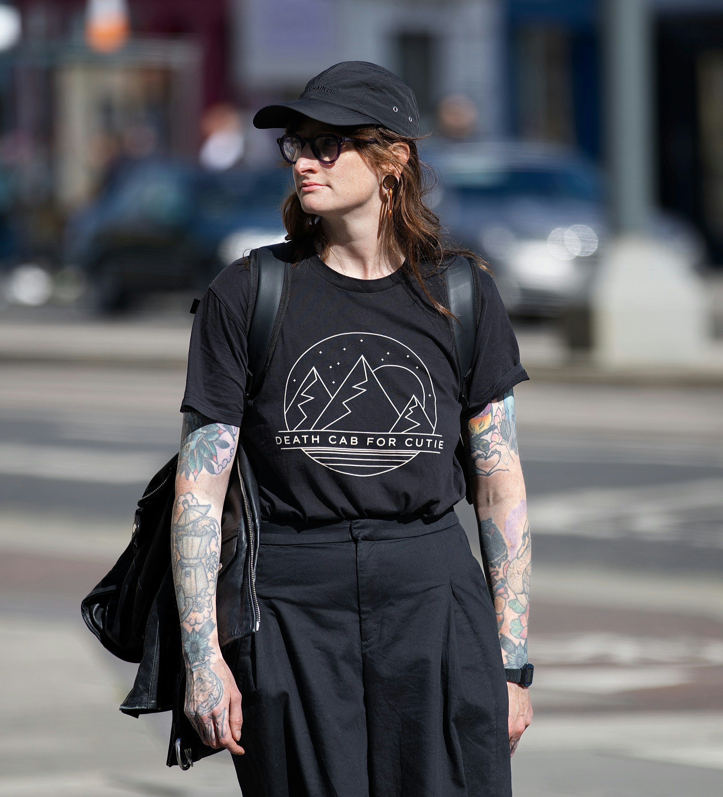 Street Portrait in Black: A Tattooed Traveler with a Canon-Ready Gaze