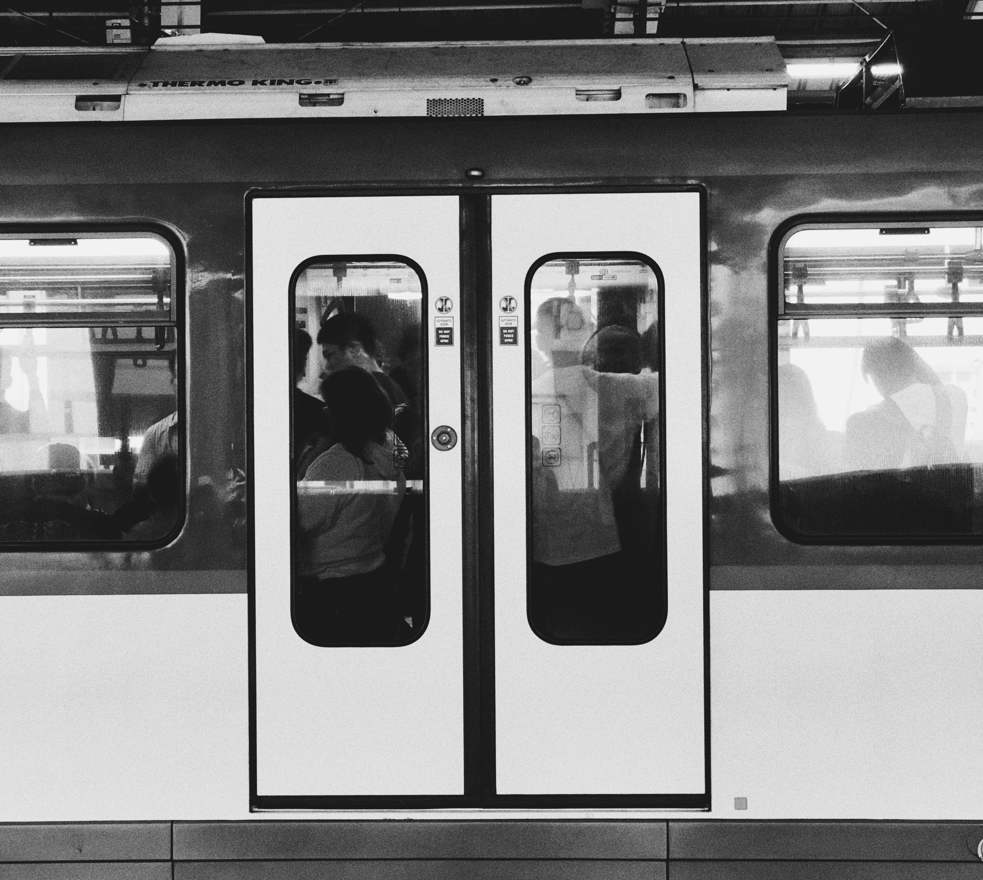 Monochrome subway doors with passengers visible through the windows, capturing a terse moment of everyday transit. (Logo/illustration not present.)