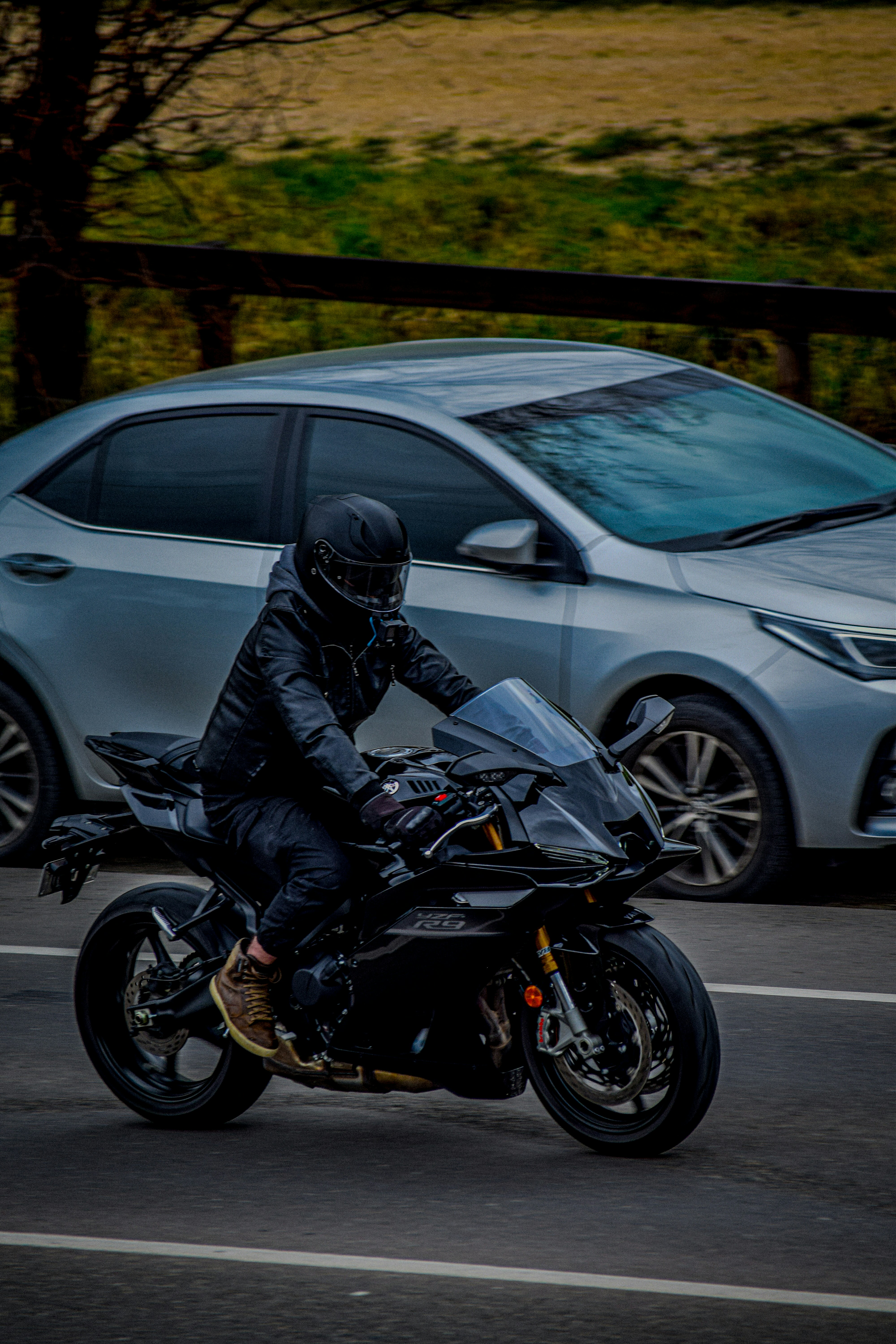 Dark-clad motorcyclist on a sportbike passes by a silver car on a dim road with blurred motion and cool tones.