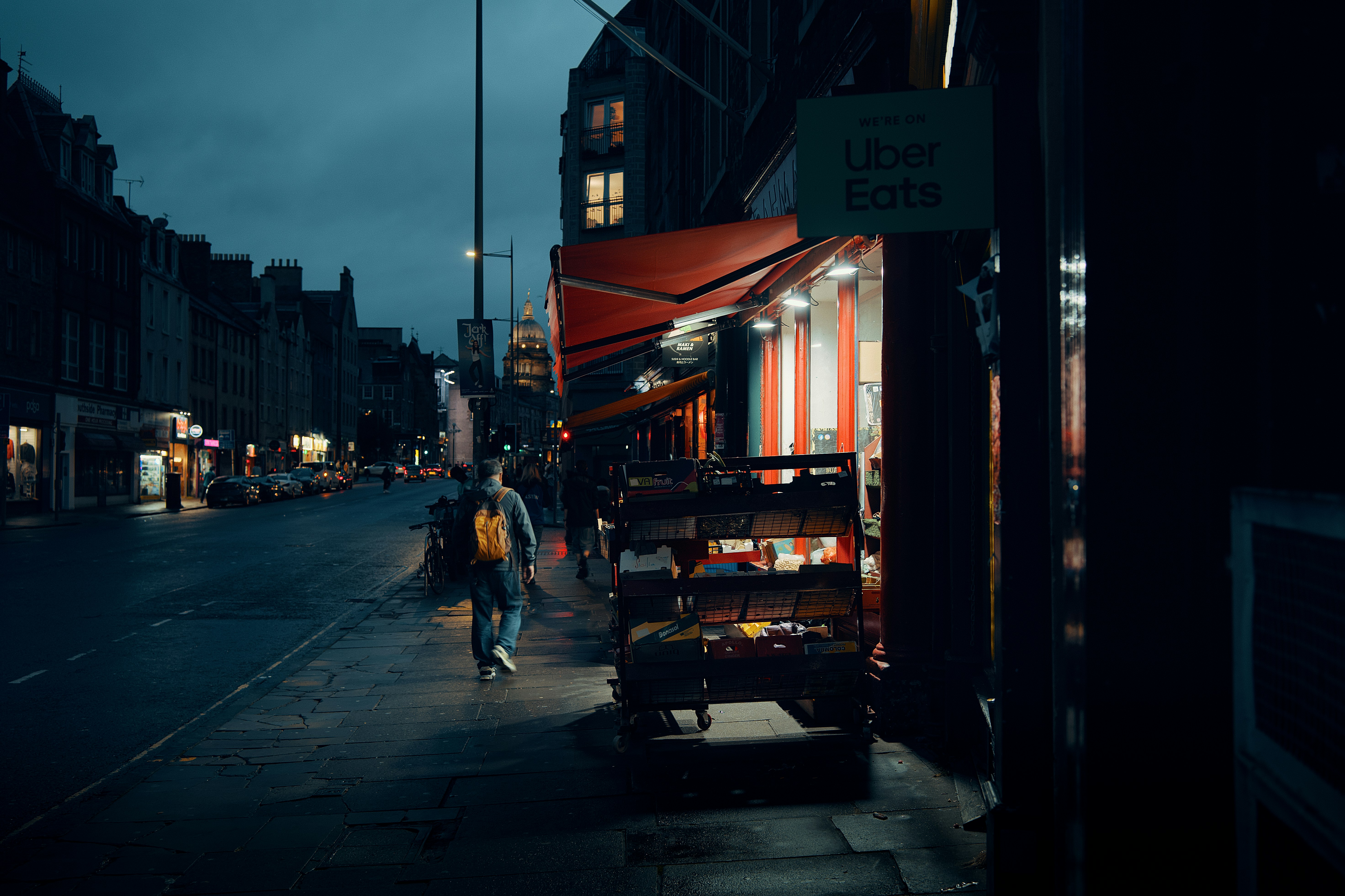 Evening Walk Past a Neon-Street Cart on a Quiet City Block
