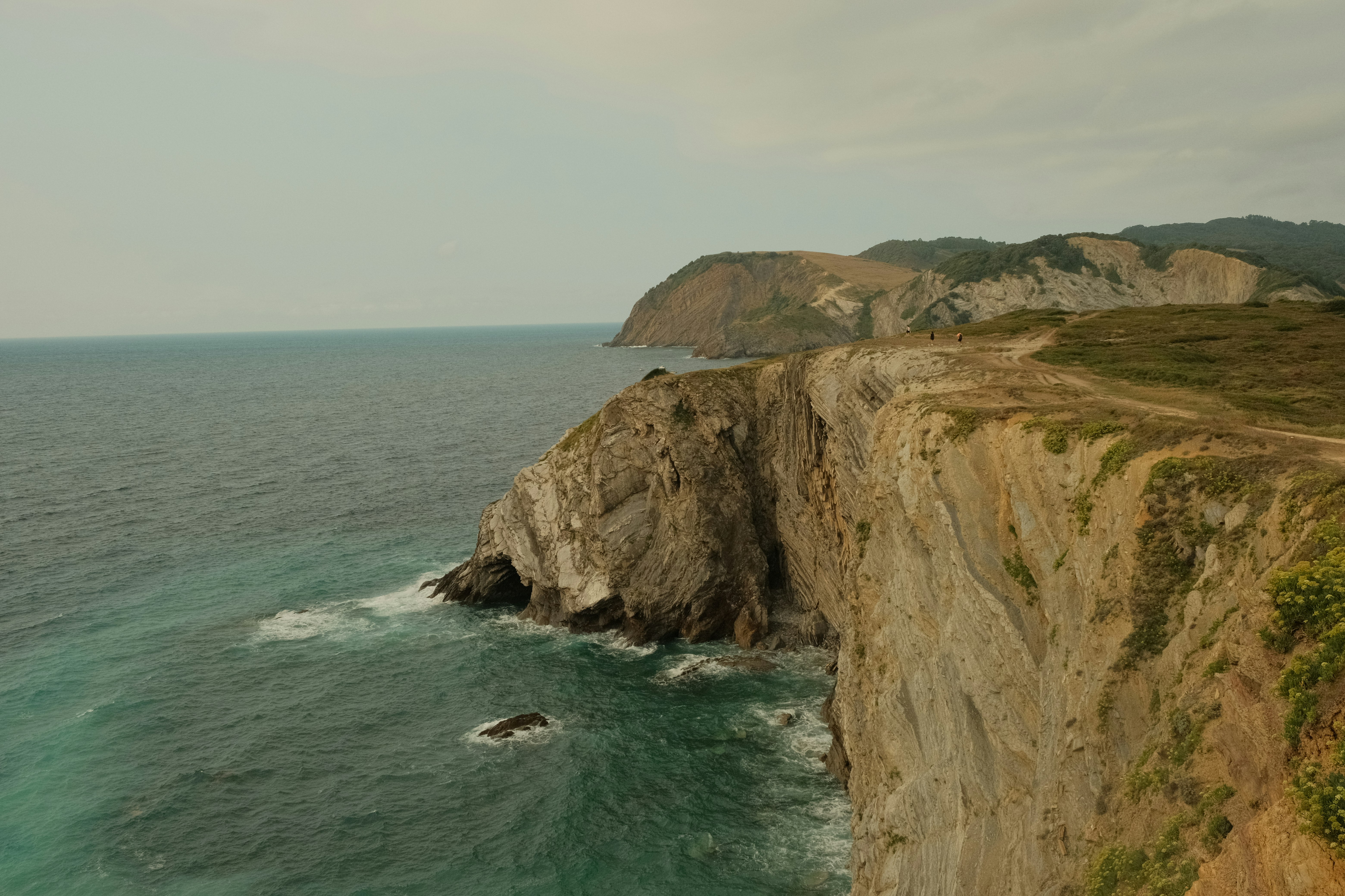 Steep rocky cliffs dropping into the sea under a pale overcast sky