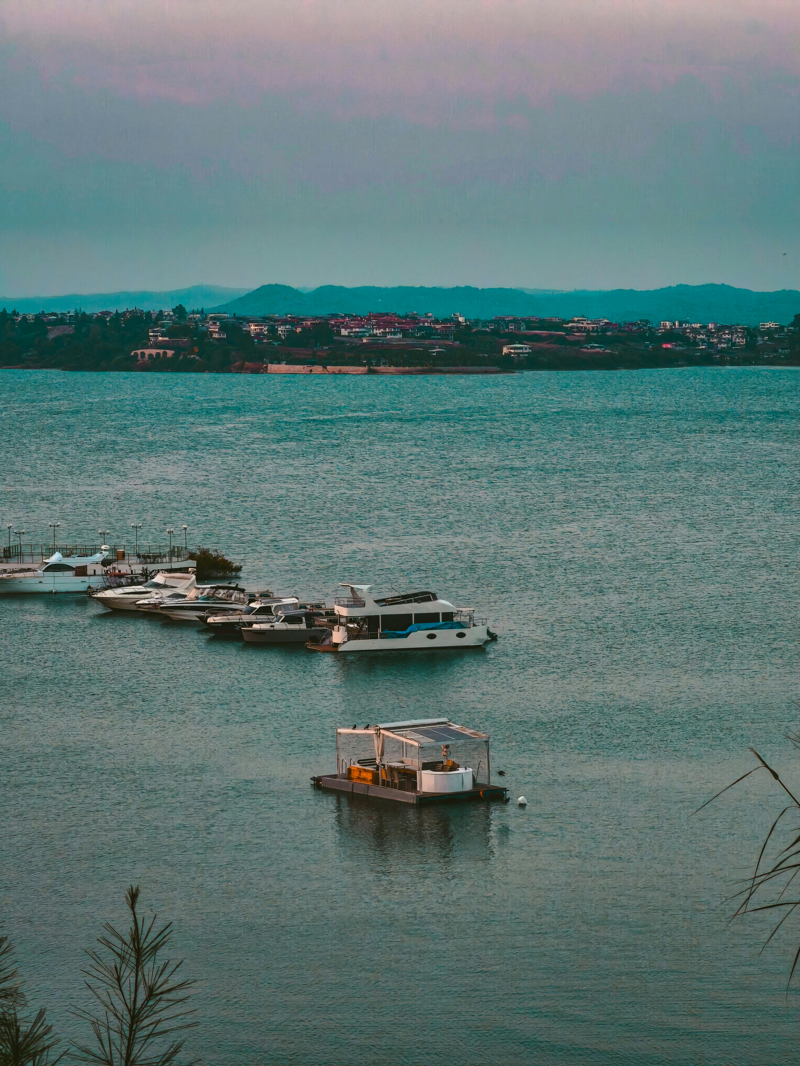 Calm coastal scene with a line of moored boats on turquoise water and a distant shoreline, emphasizing the tranquil harbor mood.