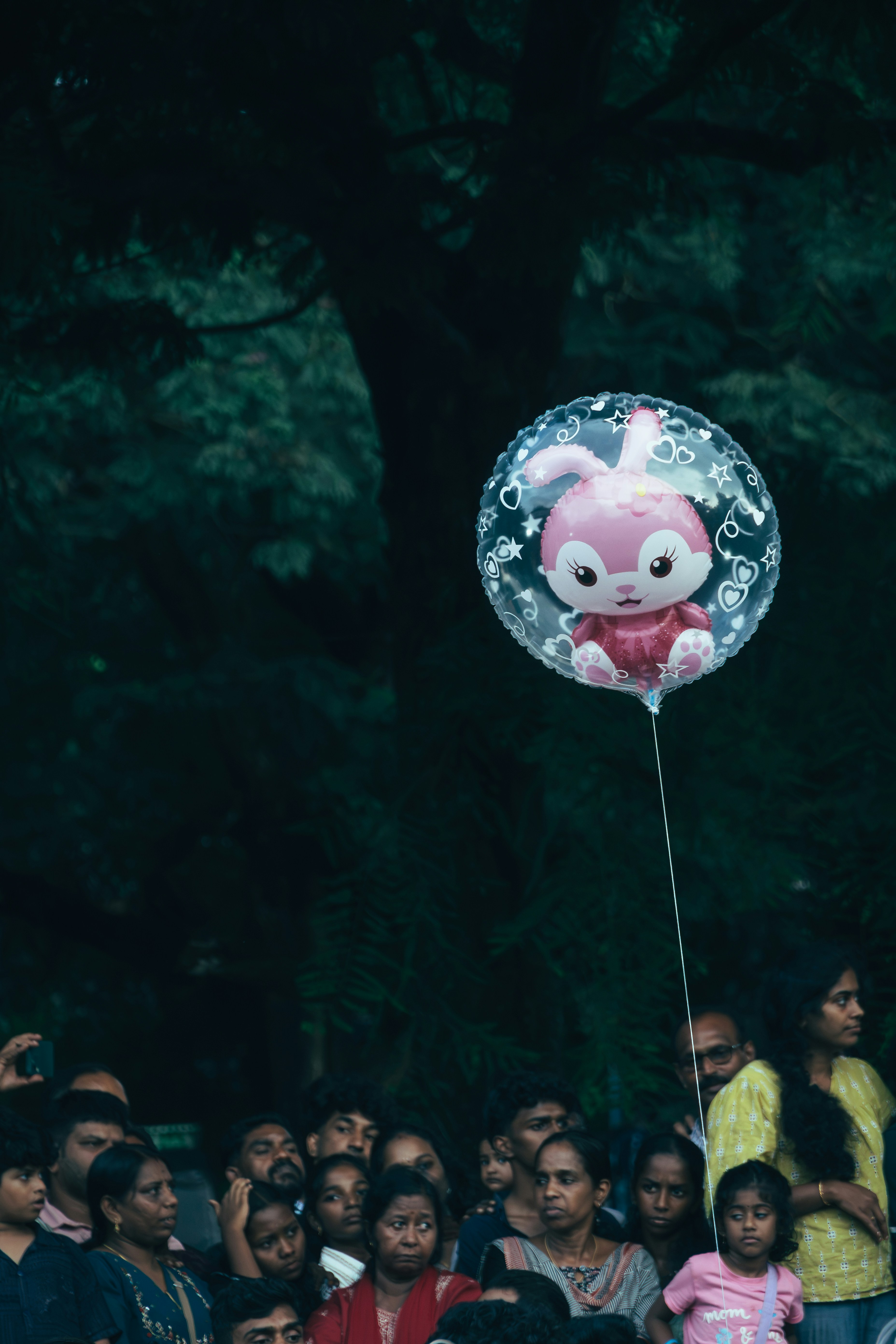 Colorful silicone balloon with a pink bunny design rising above a crowd in a garden scene.