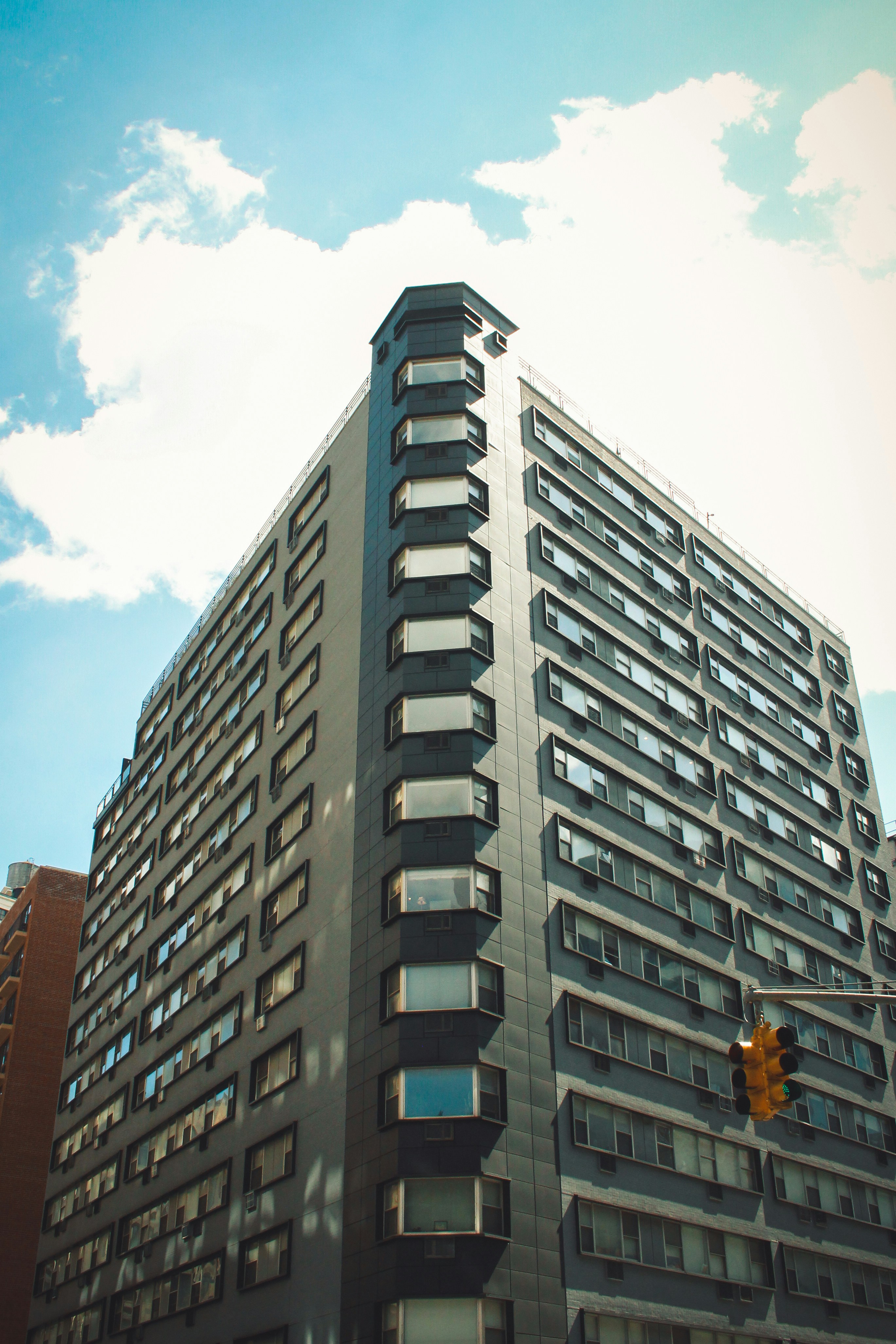 Tall apartment block angled upward against a bright blue sky, windows forming a grid across its facade; a hint of street traffic at the bottom right anchors the scene. (photography) provides architectural texture.