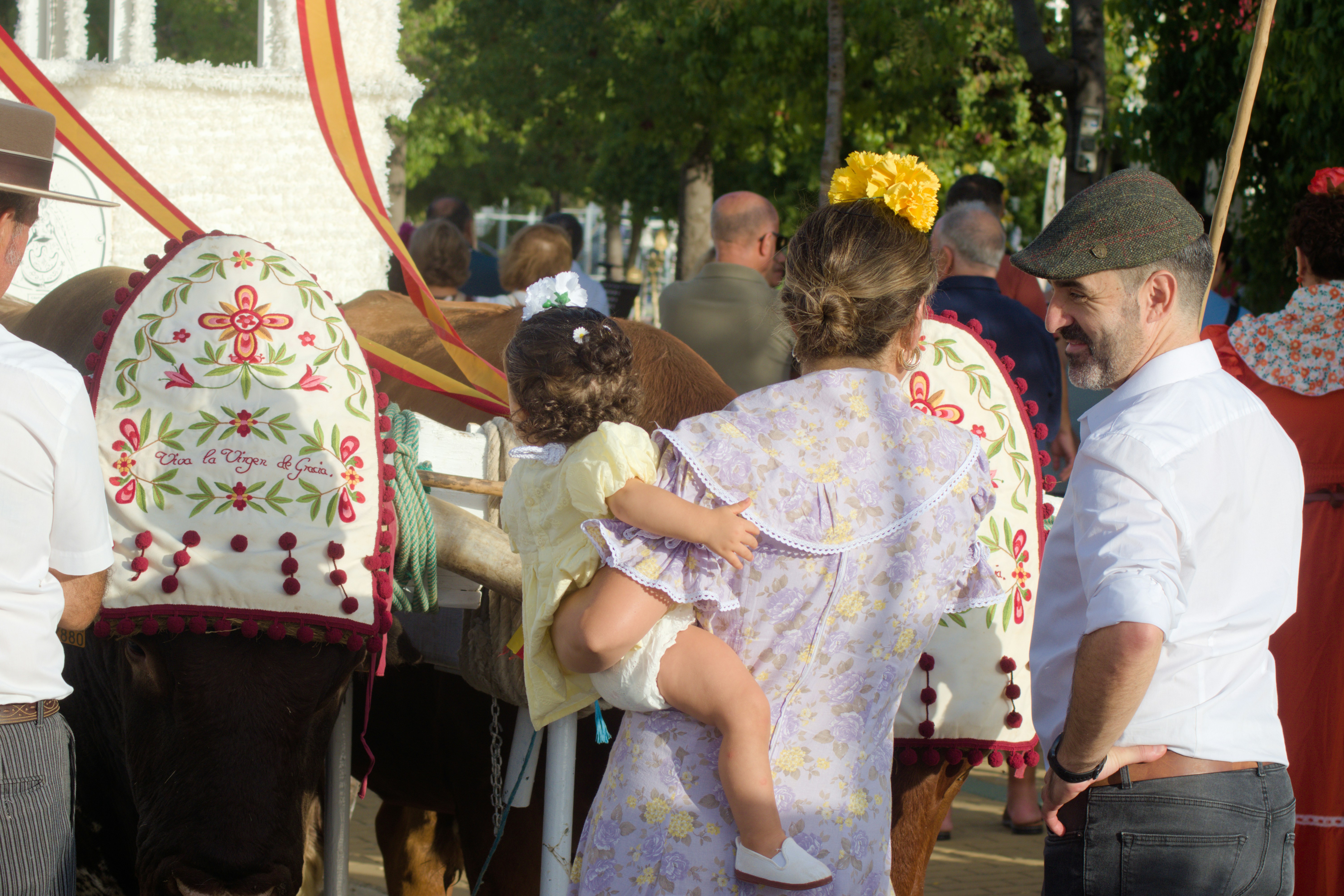 Mother in Floral Dress Holds Child Beside Colorful Parade Horses