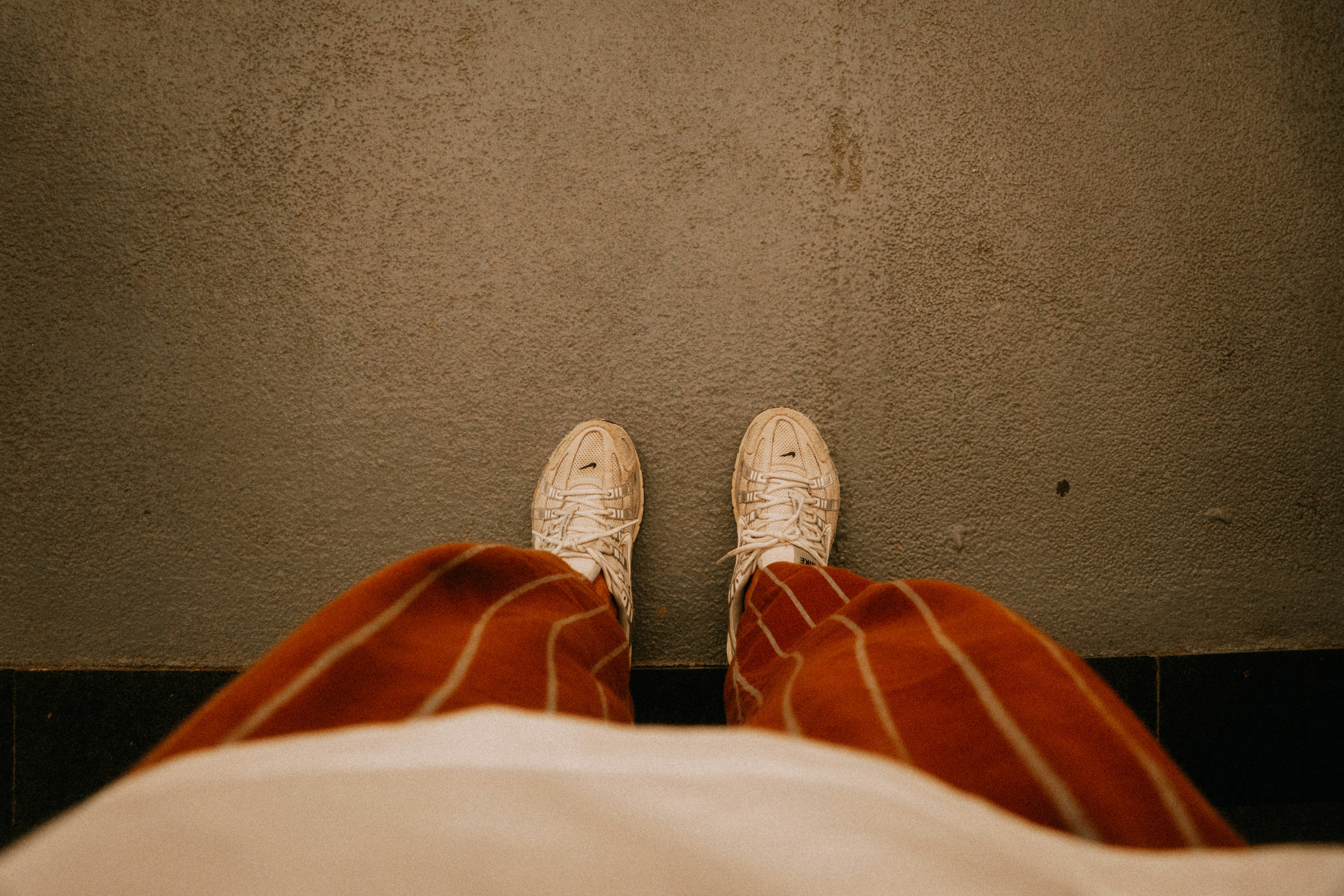 Centered steps: a top-down view toward white sneakers on a striped red sky