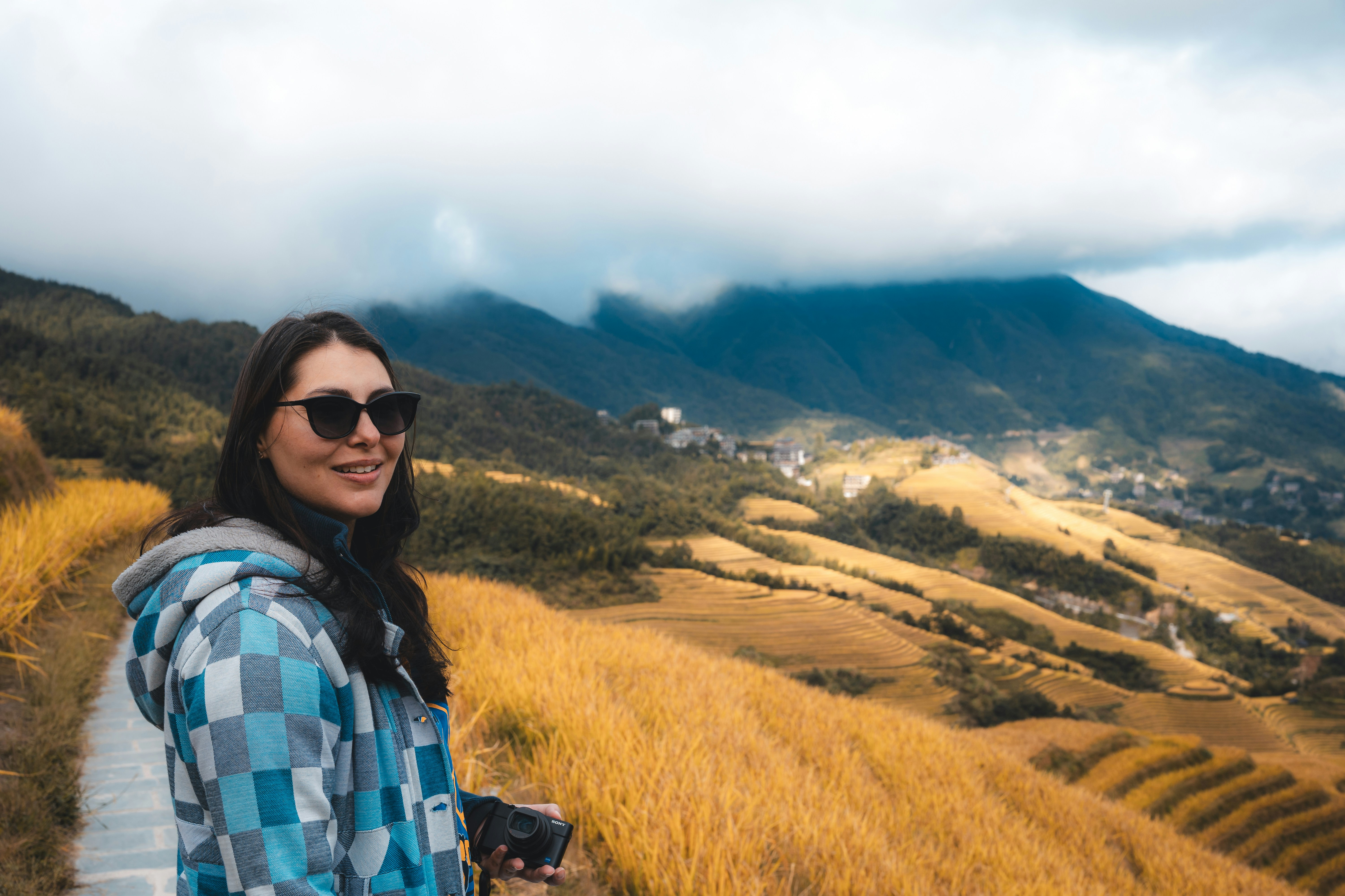 Woman in a Checkered Windcheater Overlooking Terraced Hills under Cloudy Sky