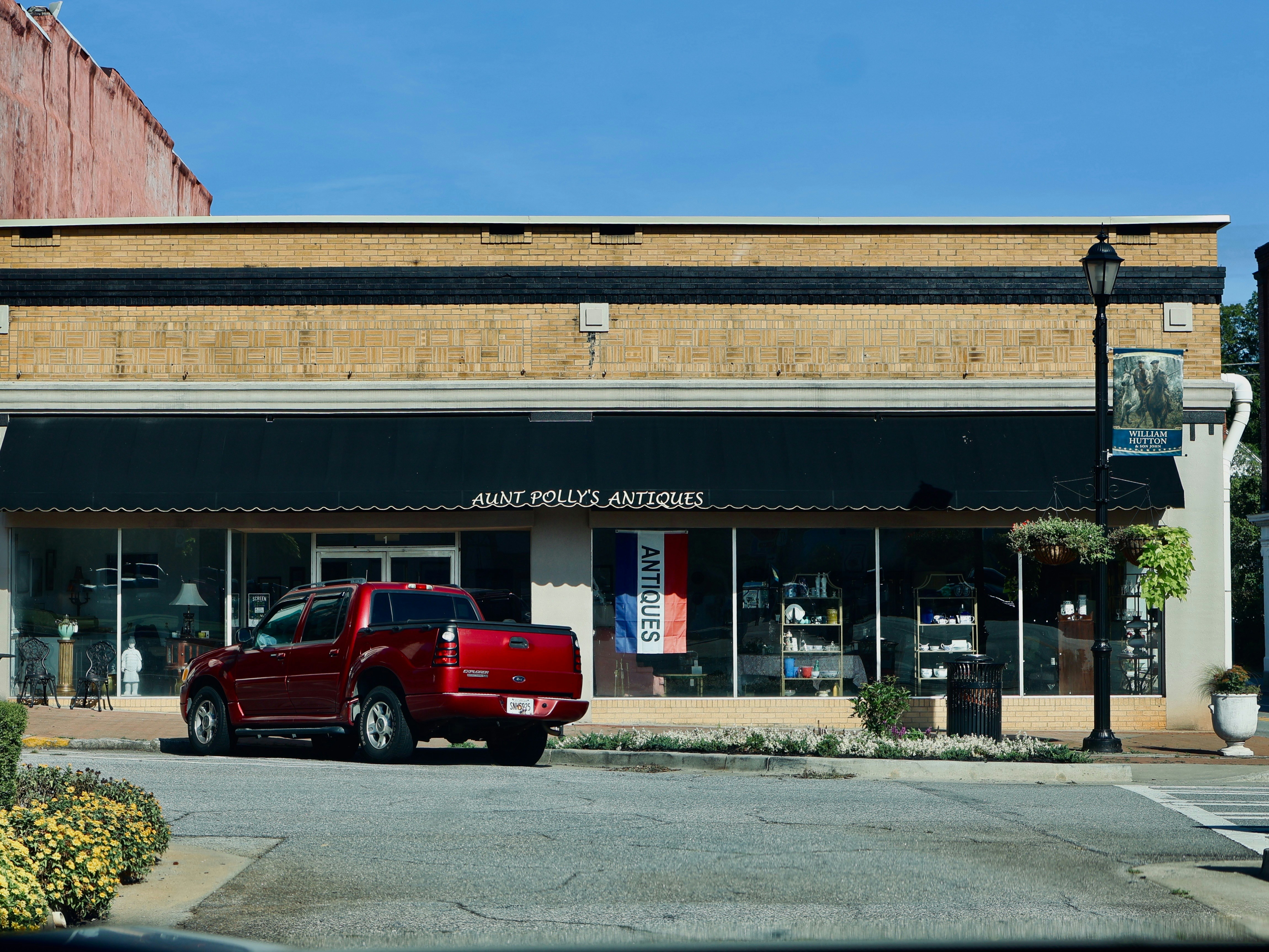 Red pickup parked in front of a quaint antiques storefront with a black awning on a sunny day in a small town.