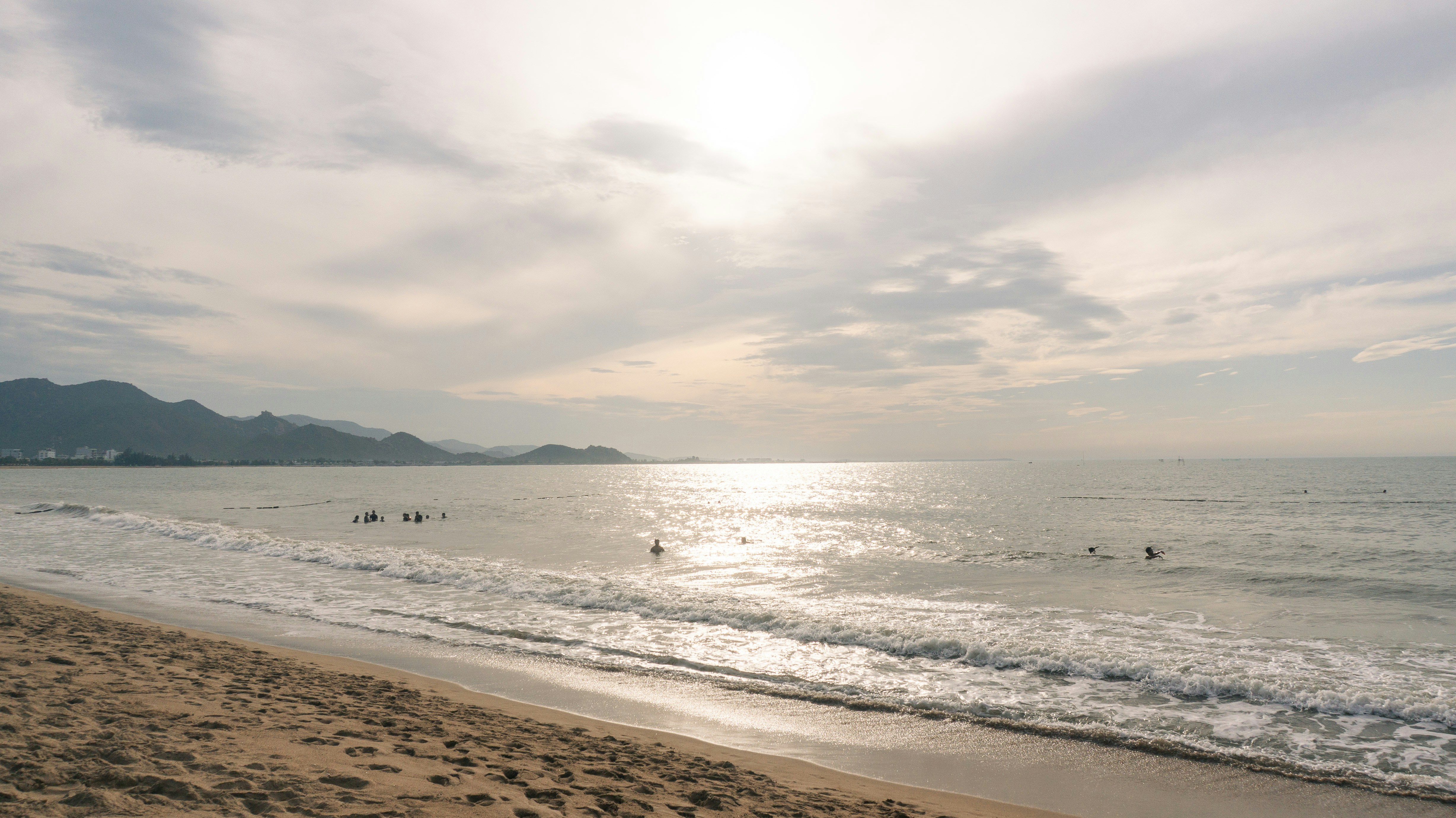 Soft sunset over a tranquil beach with gentle waves and distant mountains, capturing a calm seaside scene.