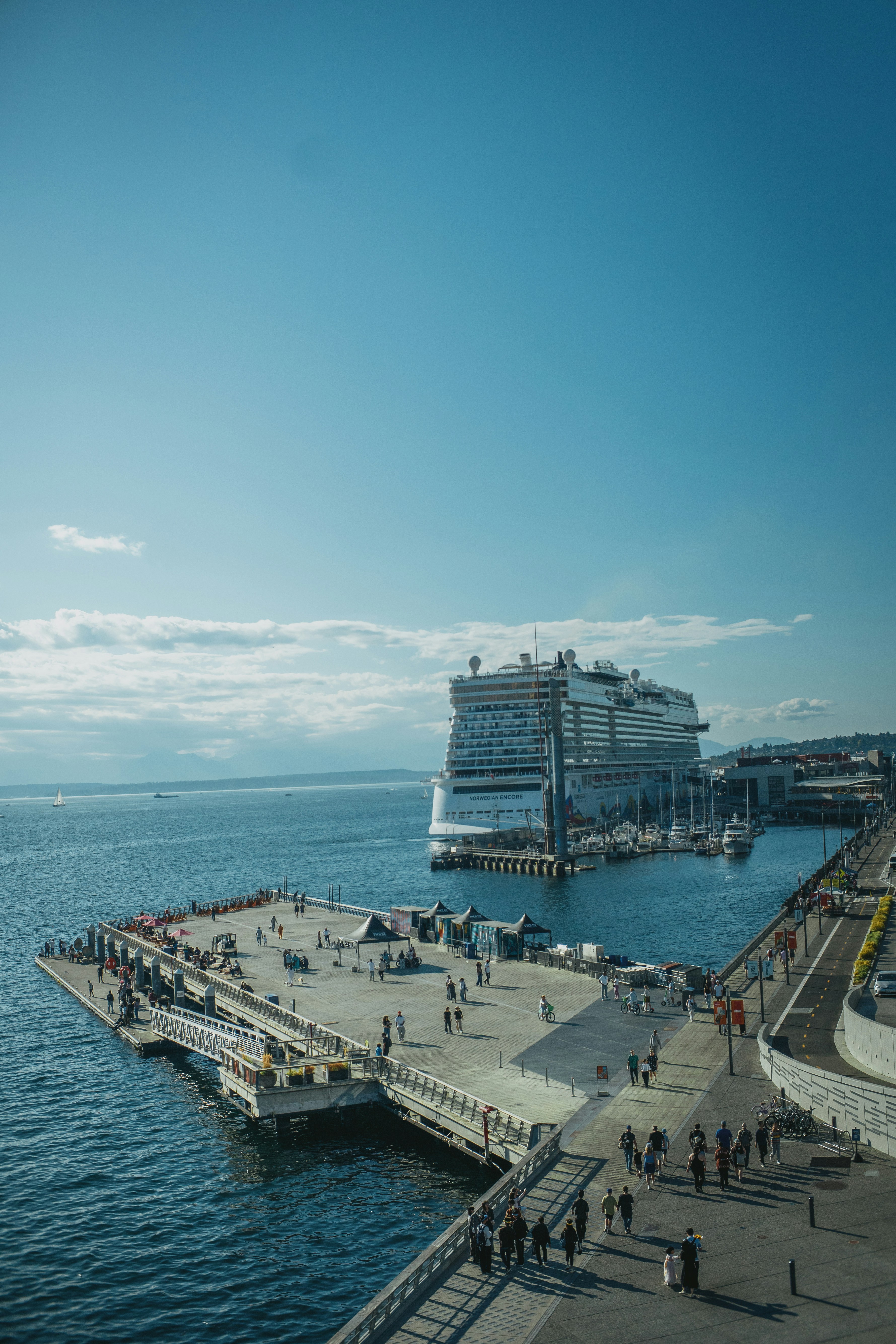 A large cruise ship docked at a pier with people walking on the waterfront