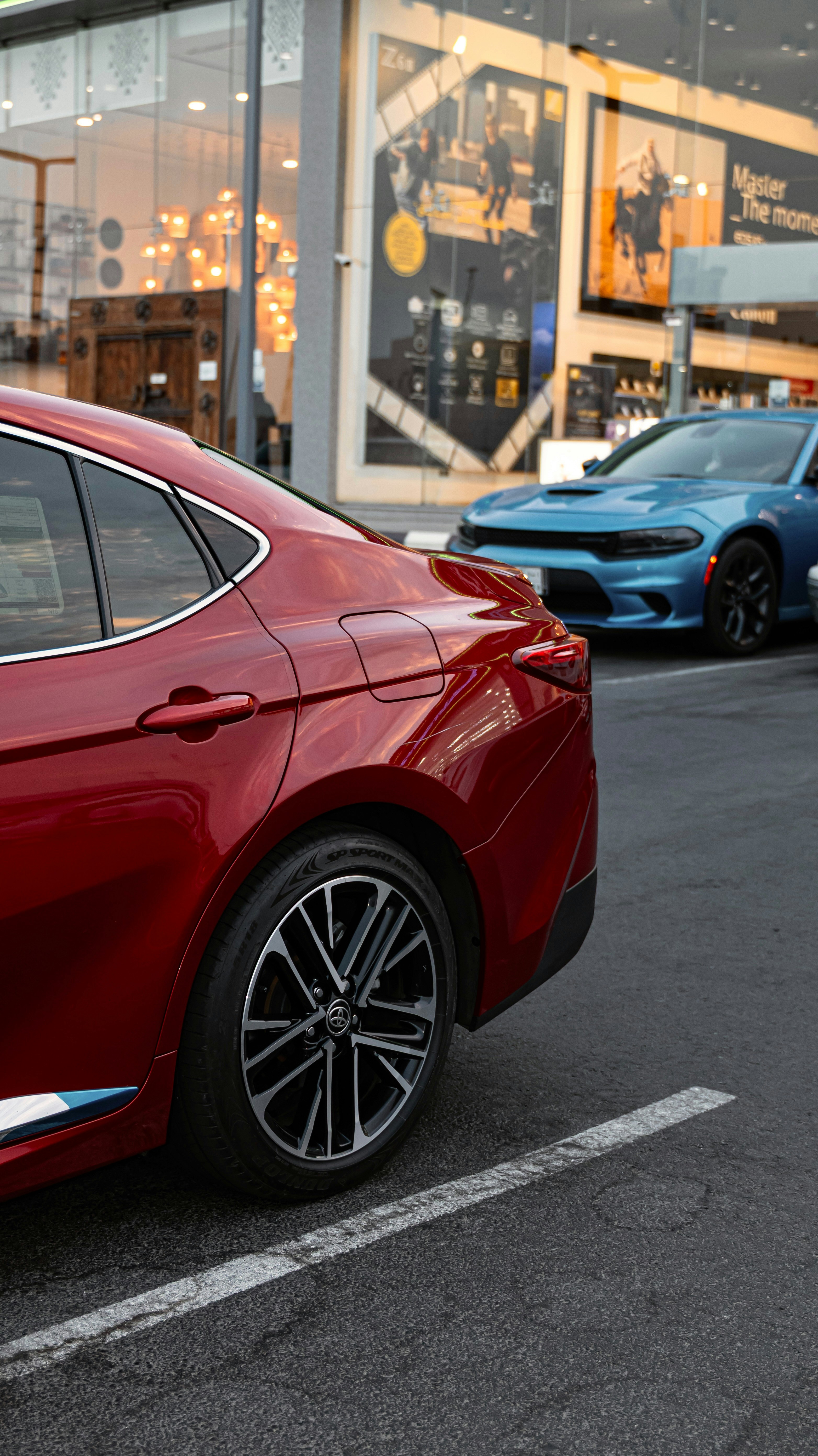Rear Quarter Hour: A Red Sedan with a Blue Challenger Framed by Shopfront Lights