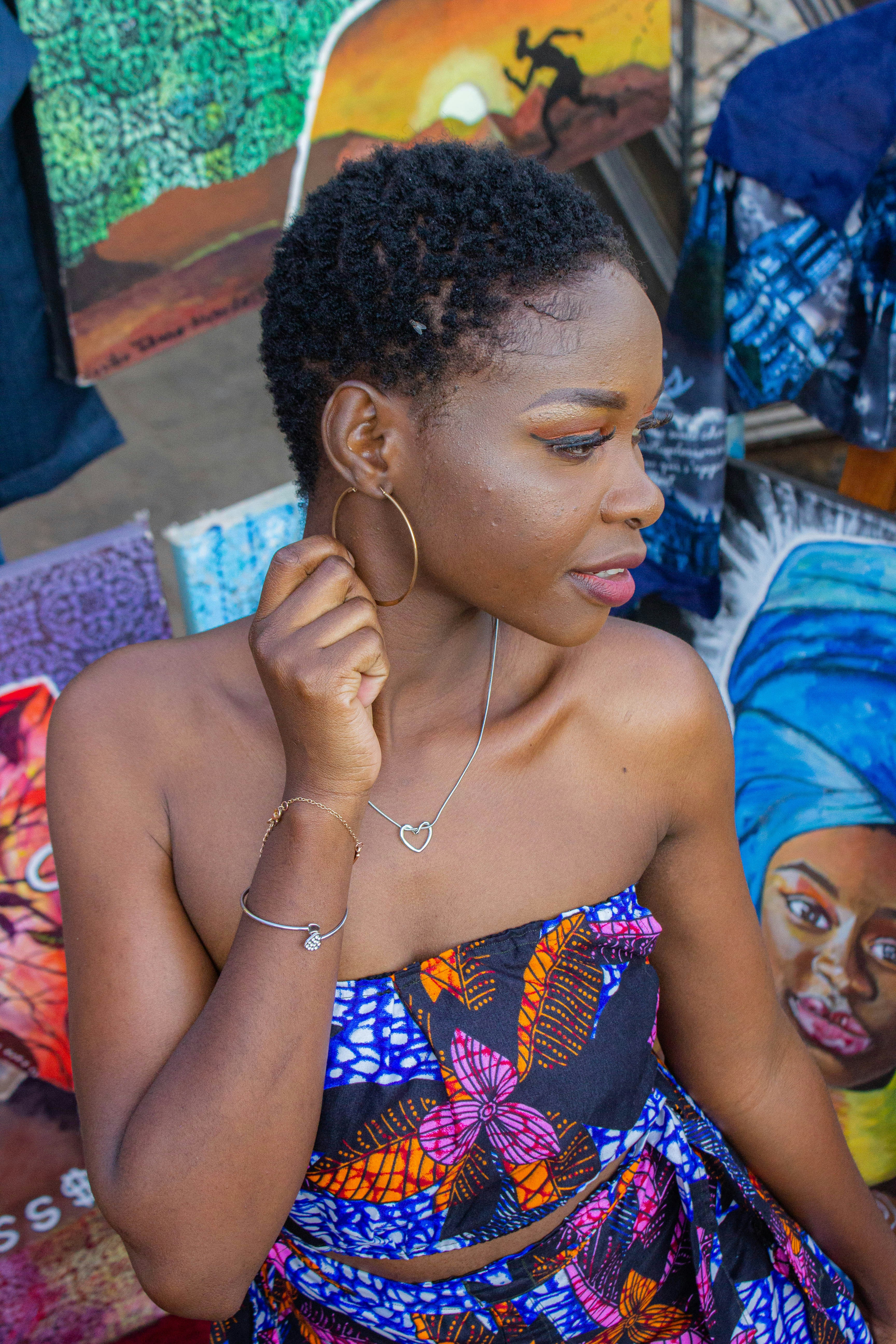 Portrait of a woman with short natural hair in a colorful patterned outfit, posing in front of vibrant murals and textiles.