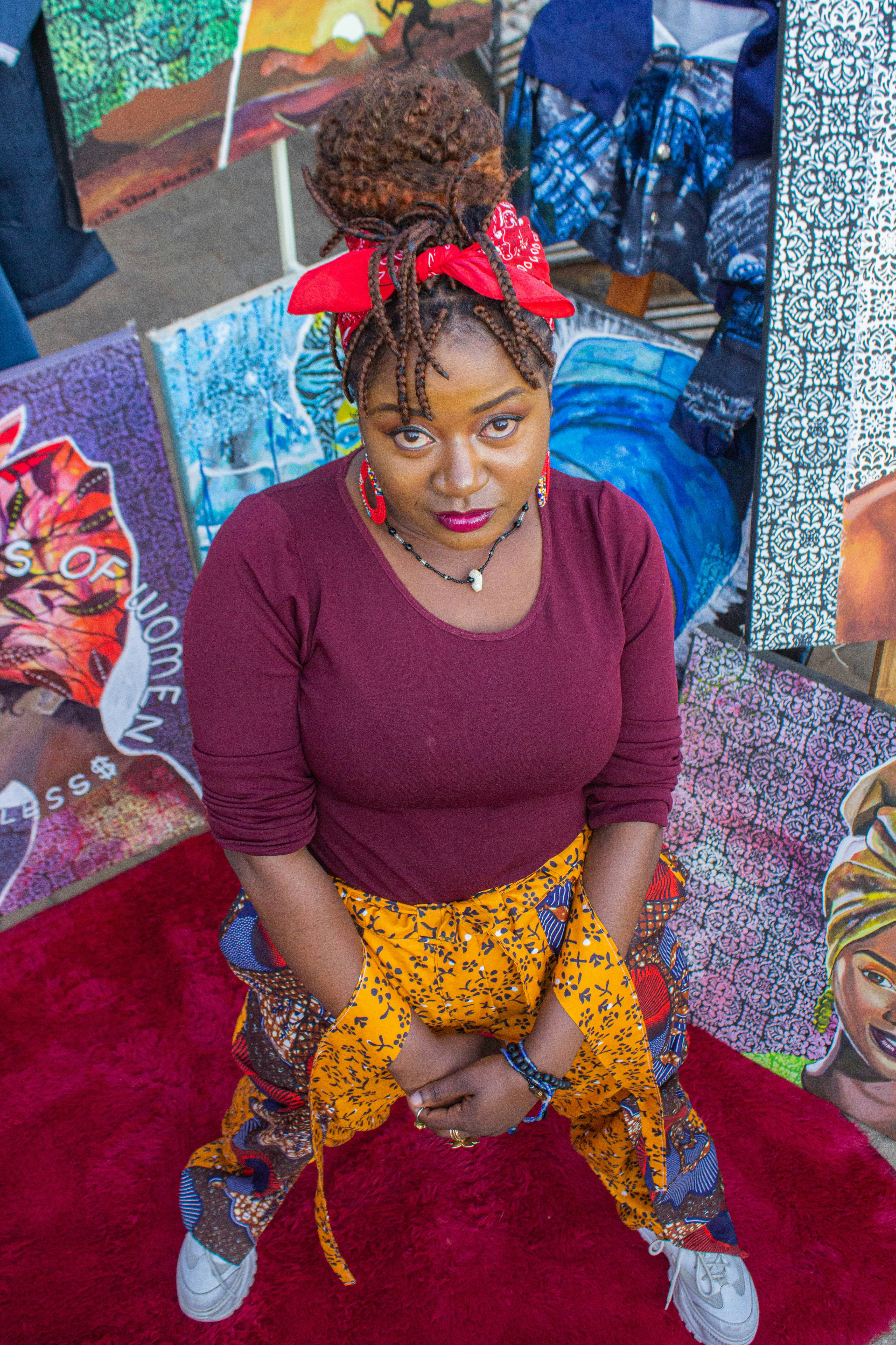 Portrait in a Colorful Marketplace: Woman in Maroon Top amidst Art Panels