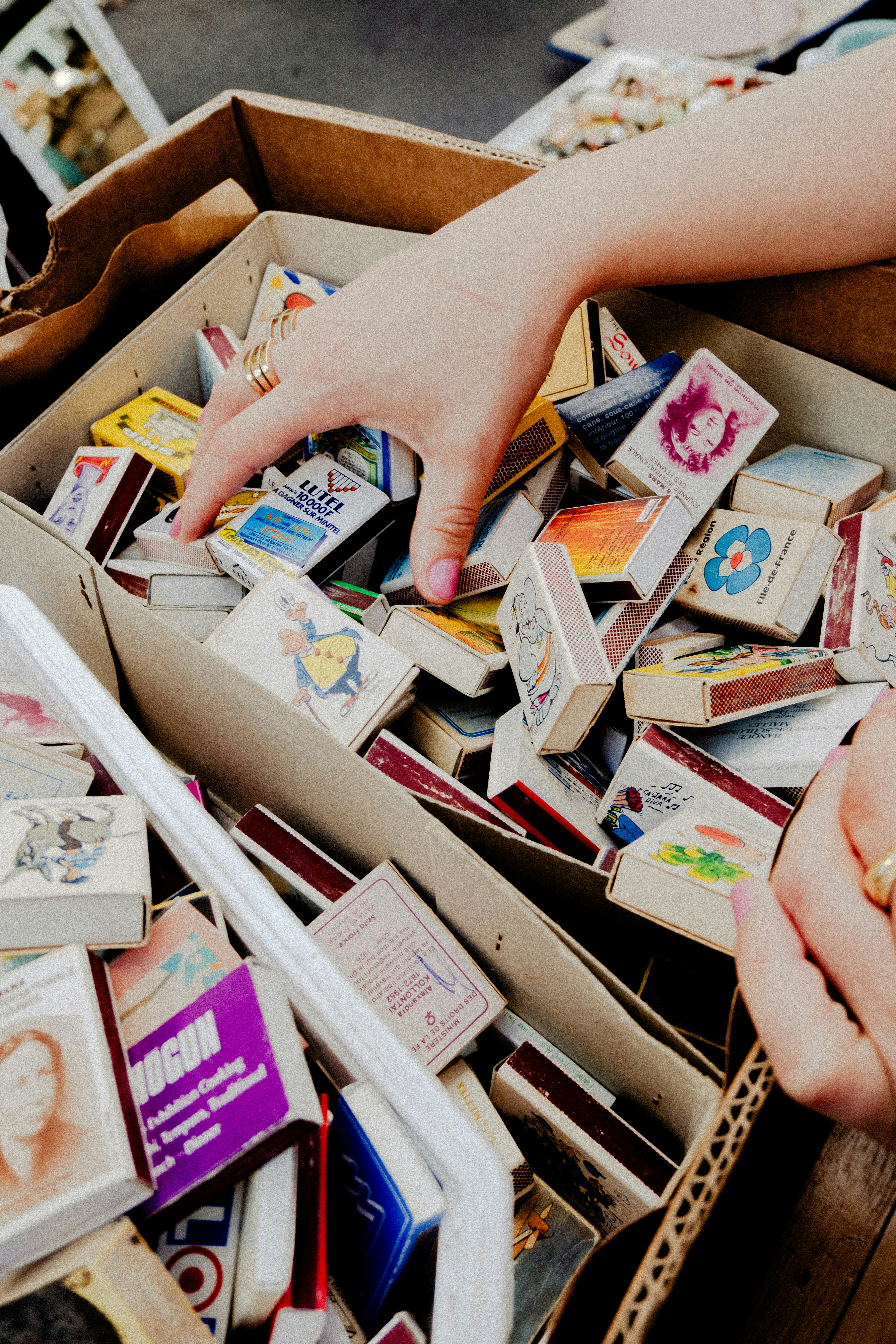 Hands Delicately Sort Through a Rainbow of Vintage Matchboxes