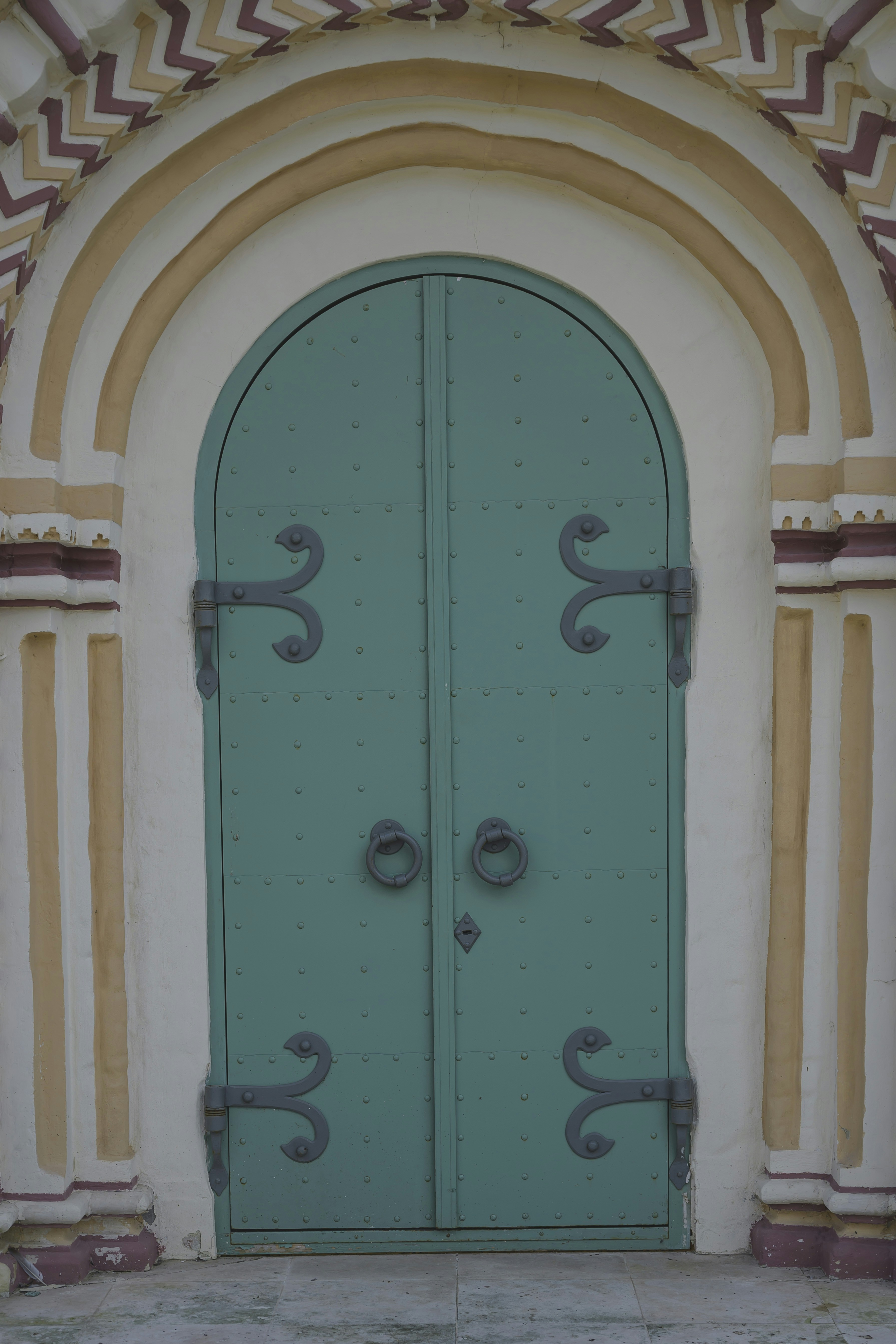 Teal Arched Doorway: A Quiet Portal Framed by Echoing Arch and Ornate Hinges